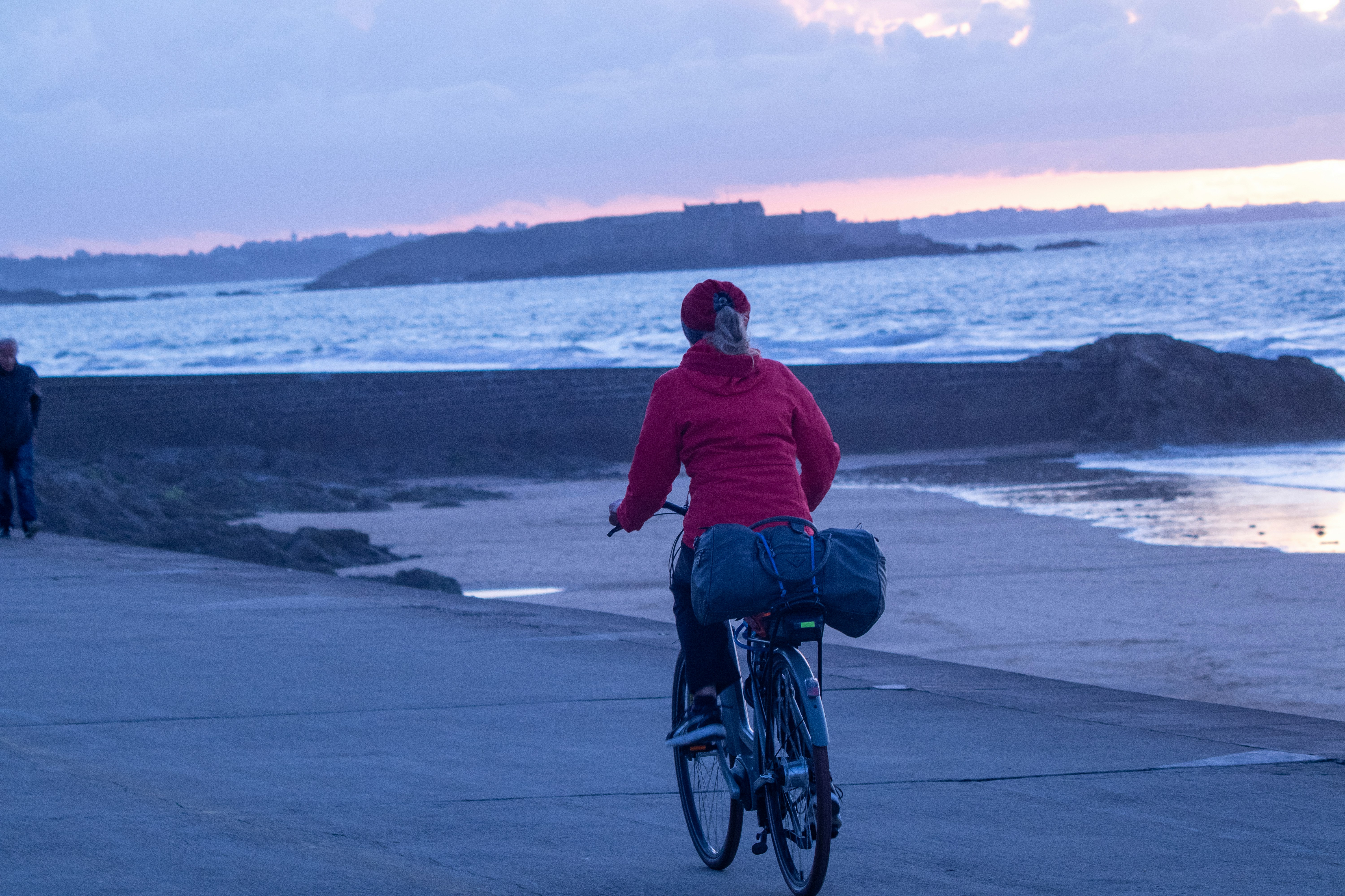 A woman riding a bike down a sidewalk next to the ocean photo – Free ...