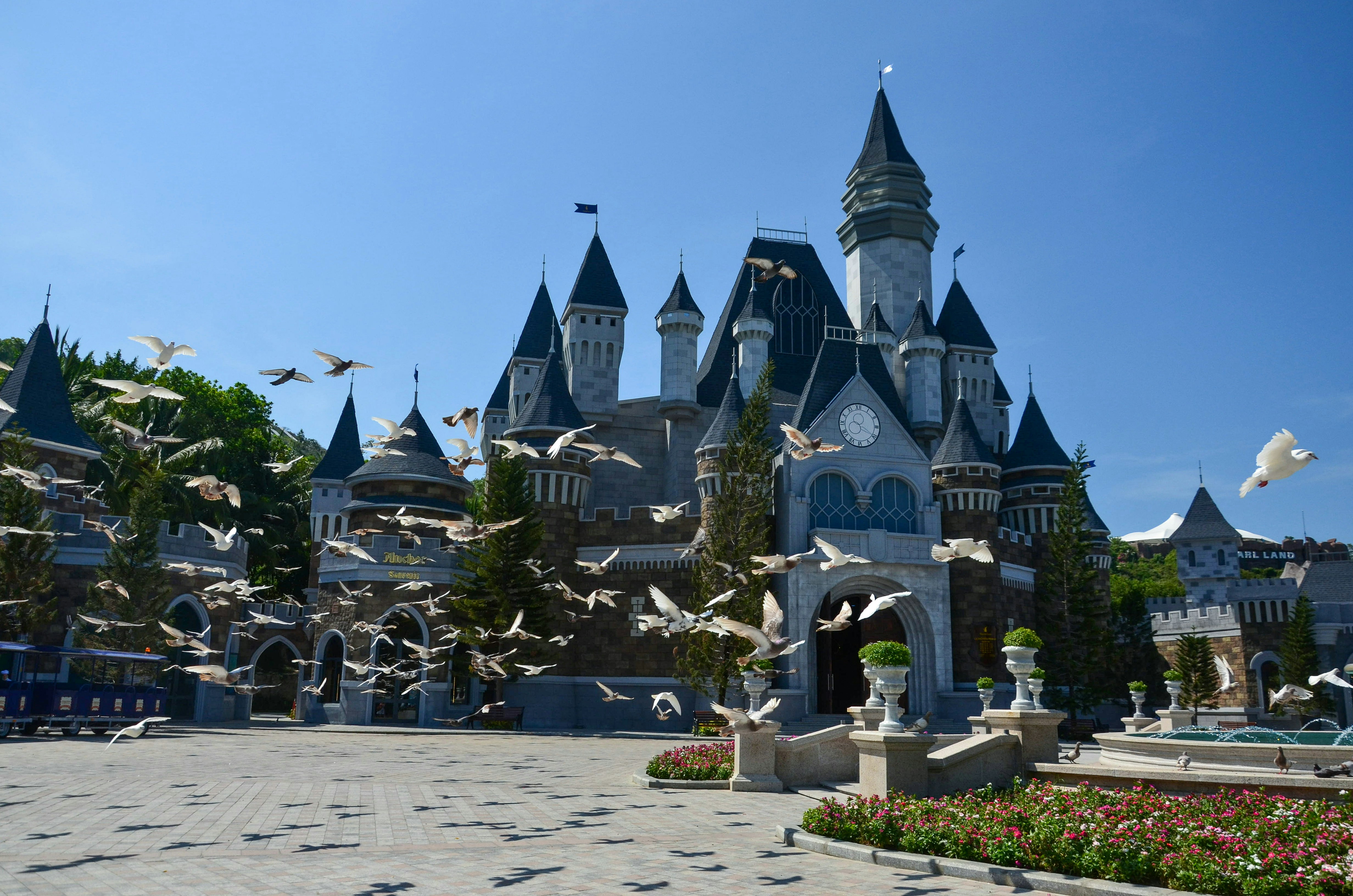 A majestic castle with turrets and spires surrounded by vibrant flowers and a flock of white doves in mid-flight.