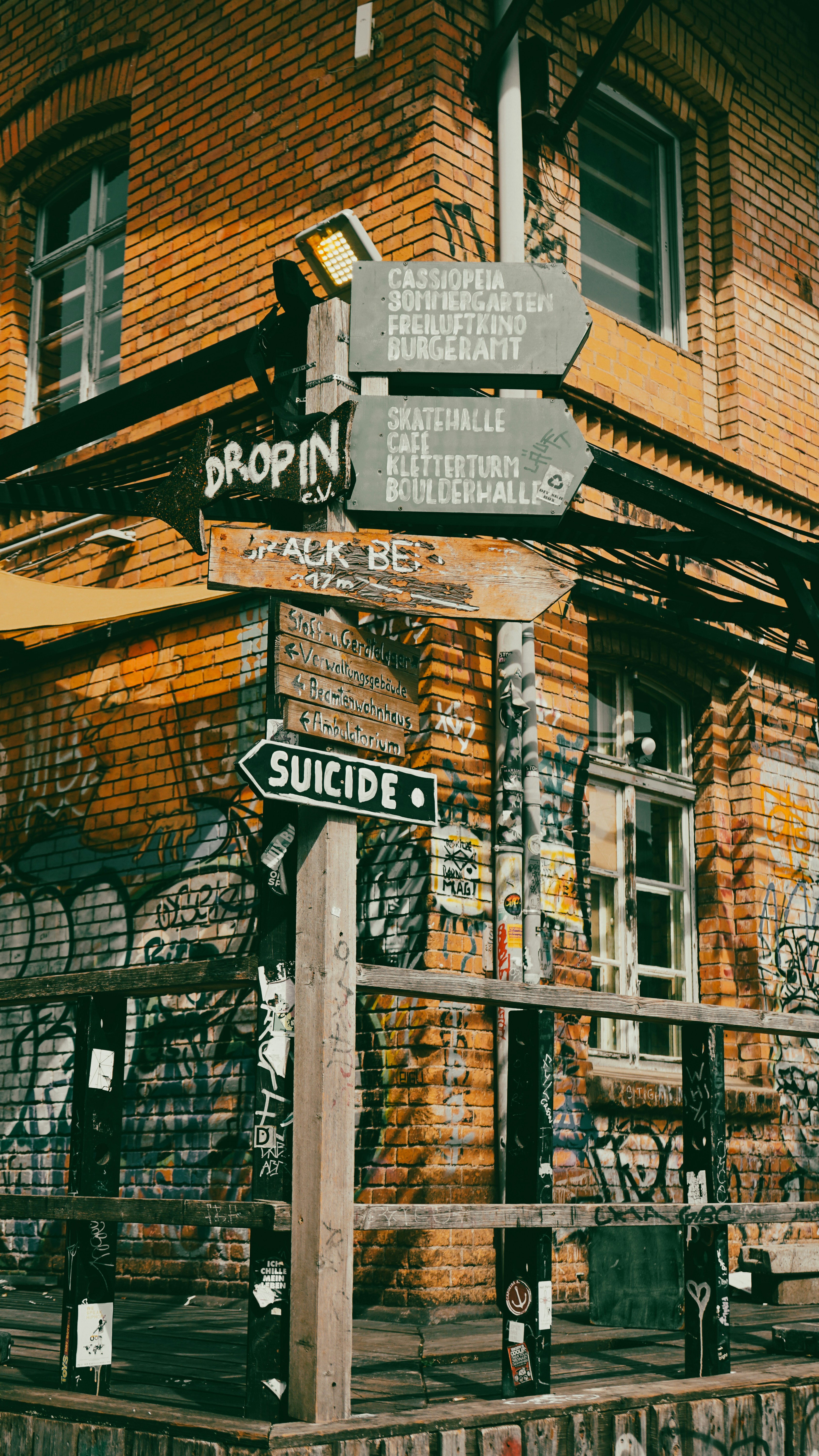 Wooden signpost with various directional arrows in front of a graffiti-covered brick wall, showcasing urban culture and art.