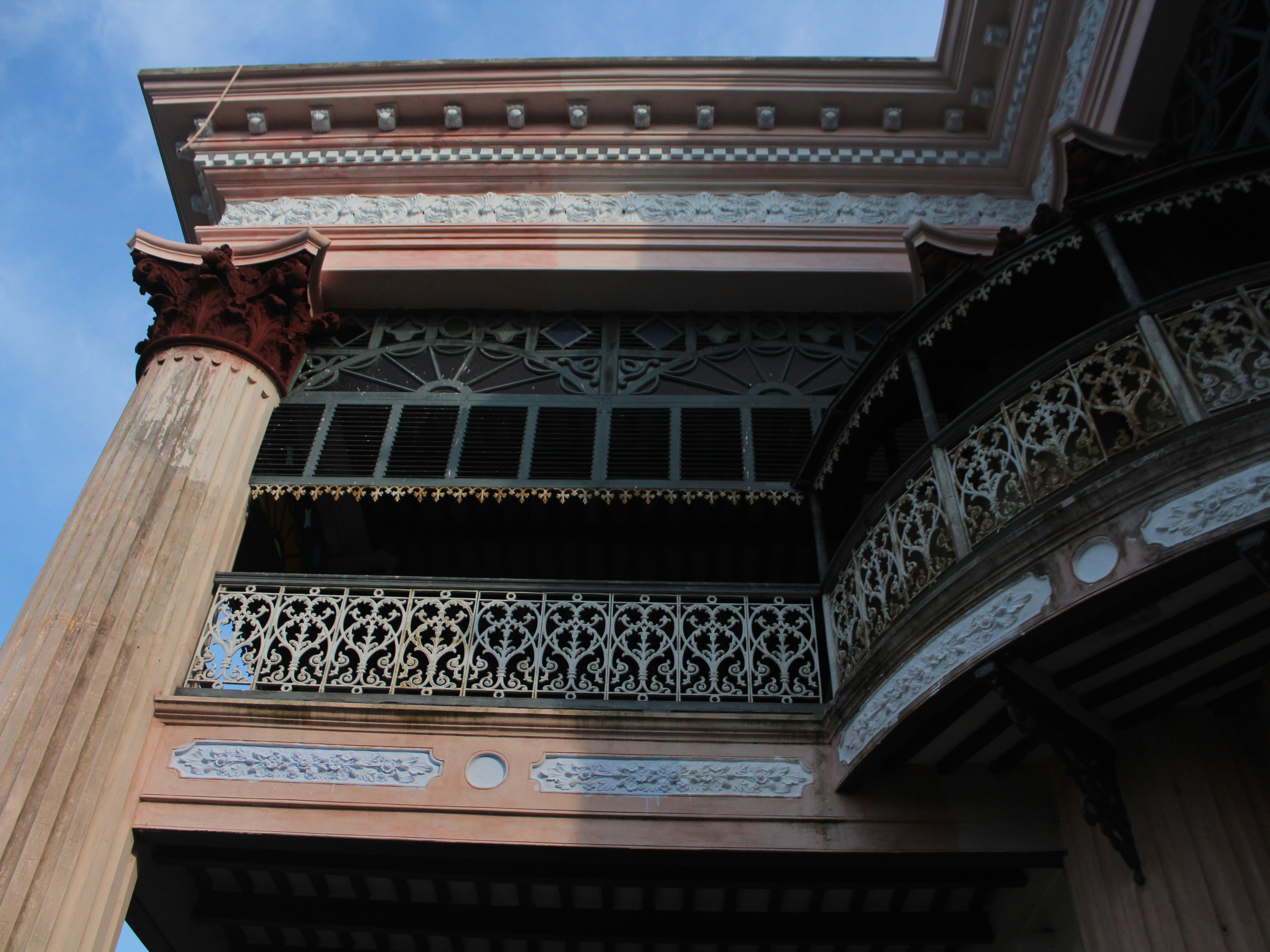 Intricate balcony and columns of a historic building showcasing ornate architectural details. The interplay of light and shadow adds depth to the structure.