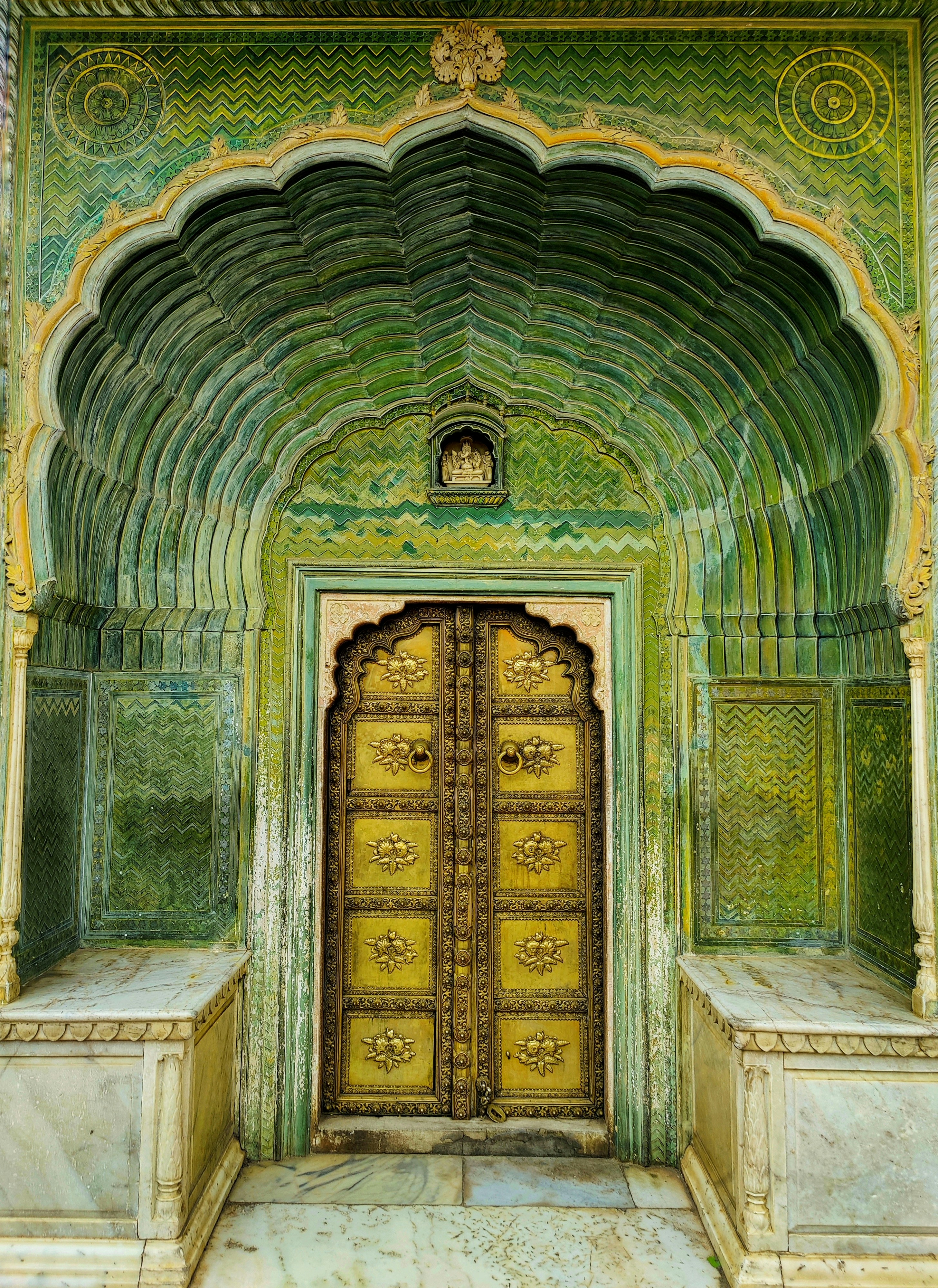 Intricately carved green and gold archway leading to a pair of ornate doors, showcasing traditional craftsmanship and historical significance.