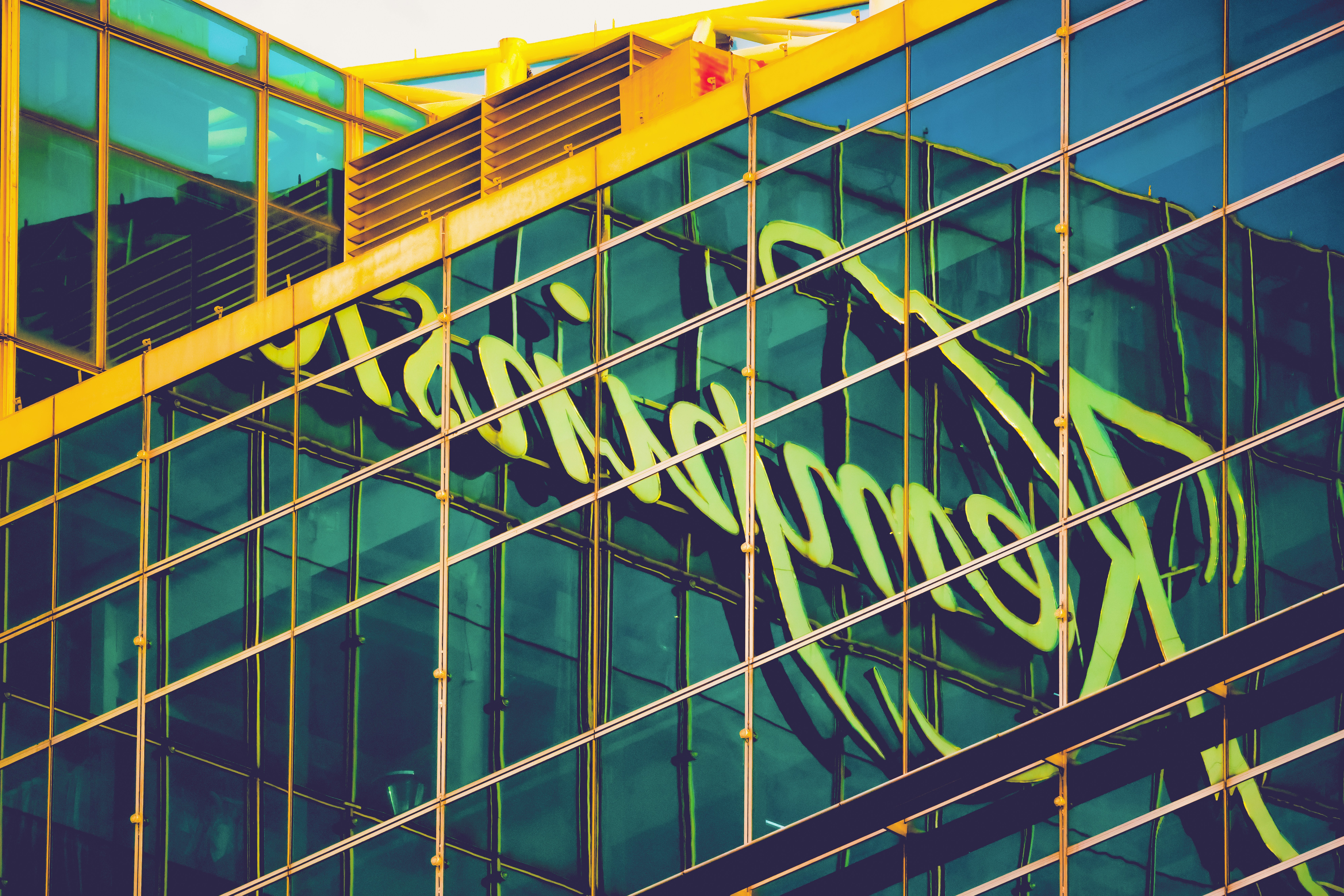 Reflection of vibrant yellow signage on a modern glass building, showcasing a blend of architecture and art.