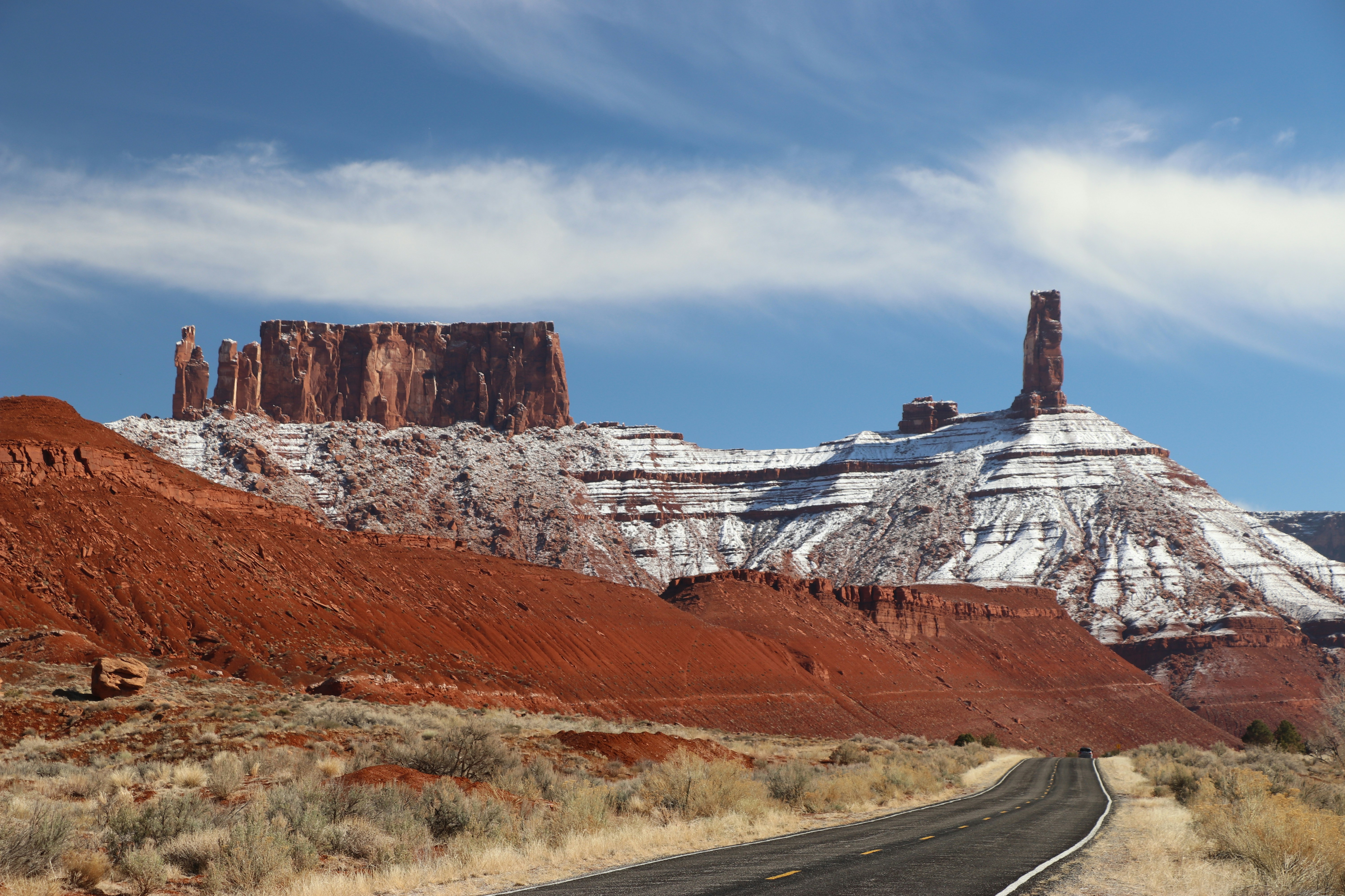 Red rock formations rise dramatically against a clear blue sky, showcasing a blend of geological history and vibrant colors. The winding road invites exploration through this stunning landscape.
