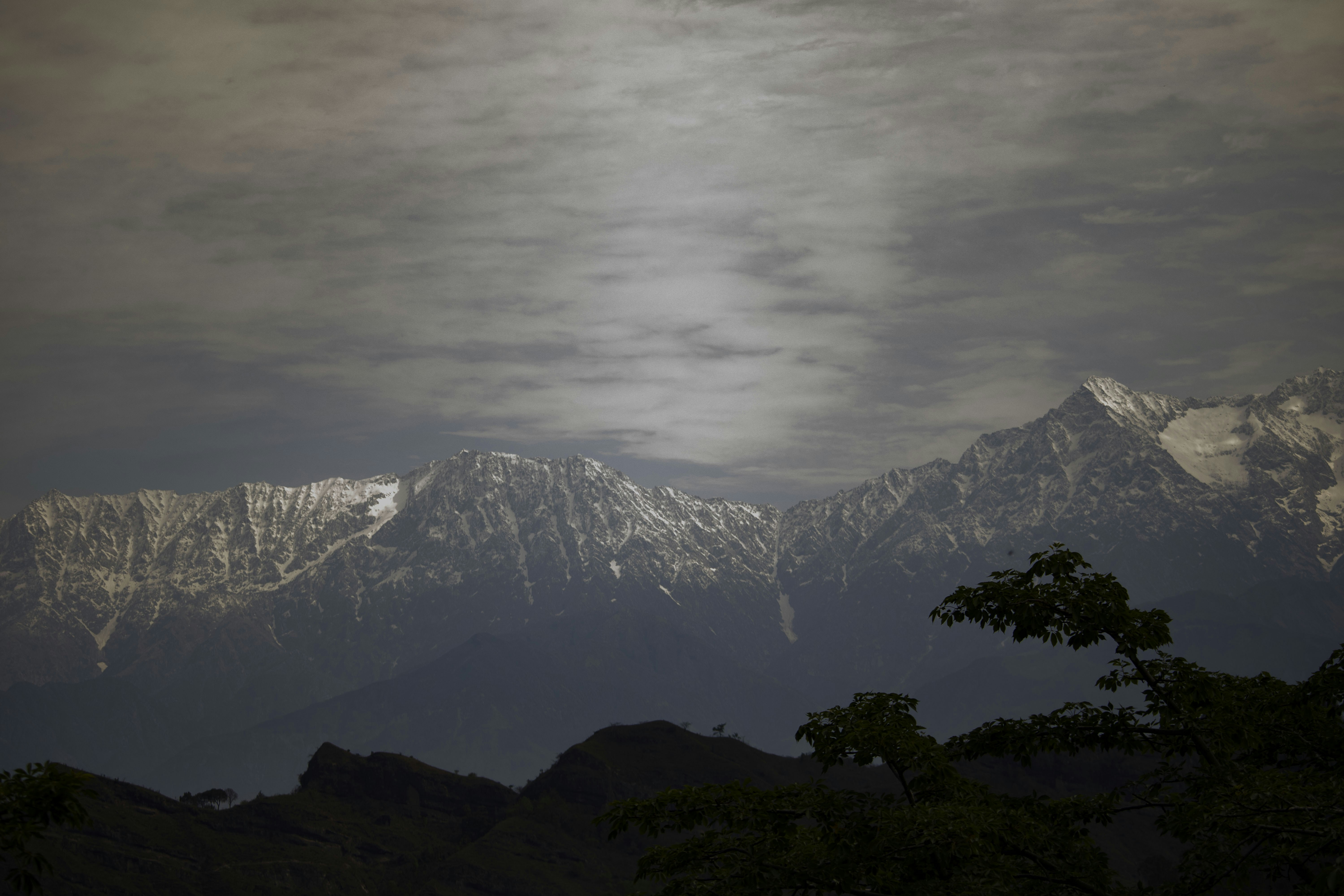 Snow-capped mountain range illuminated by moonlight beneath a cloudy sky.