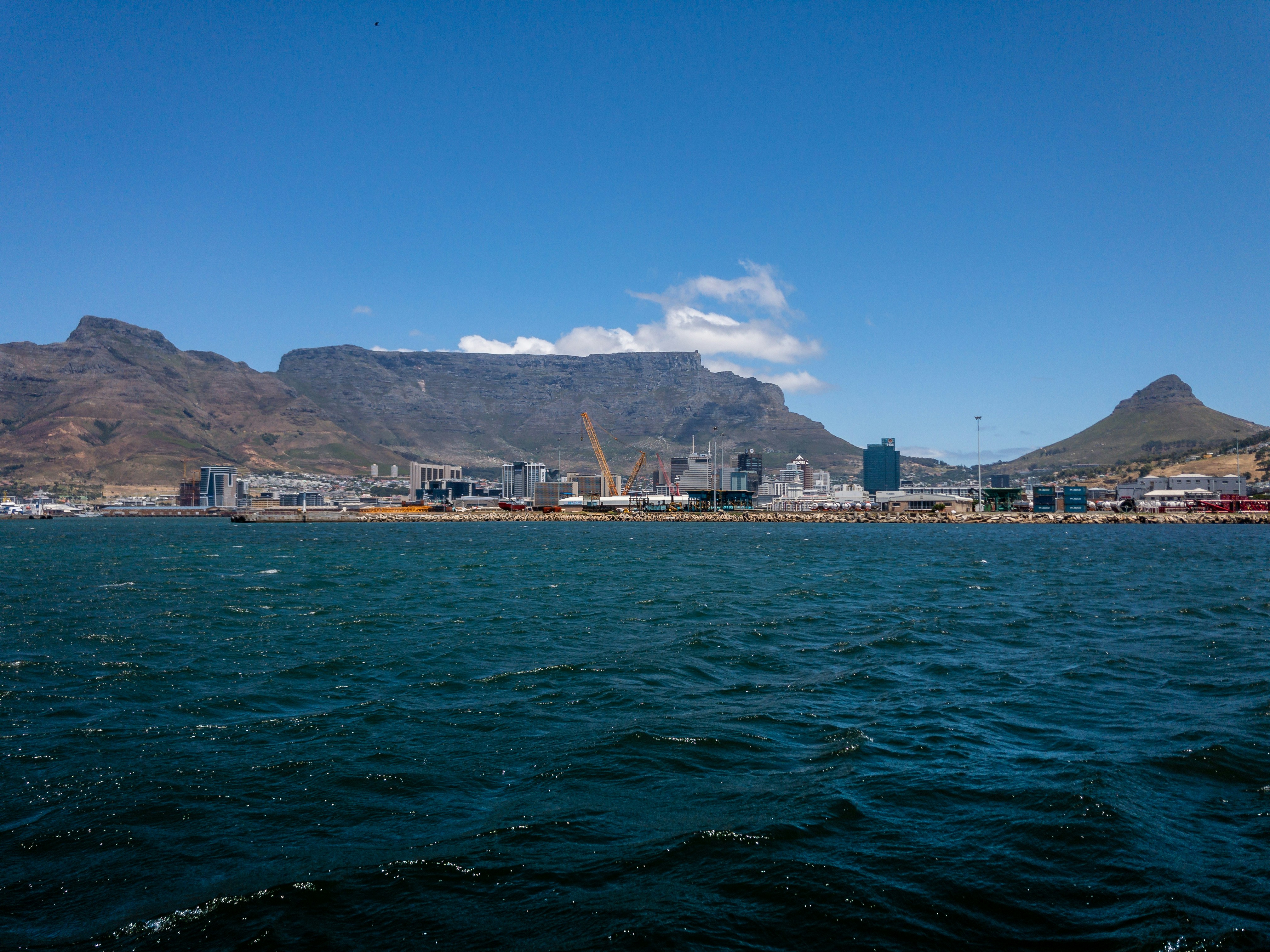 View of Table Mountain from a small tourist boat that leaves from the V&A Waterfront to show guests the views from in and around the harbour.   | a large body of water with mountains in the background
