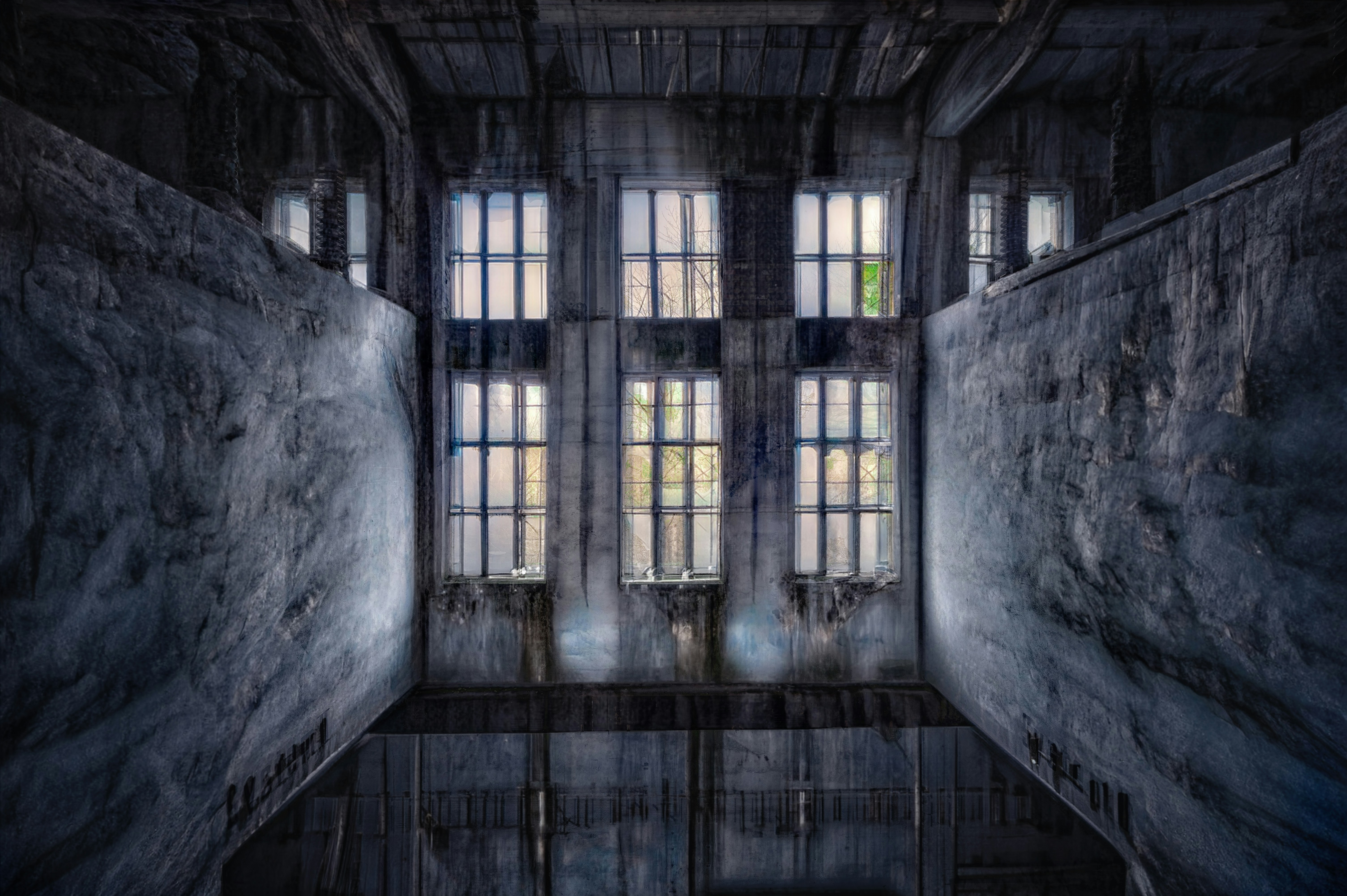 Tall, grimy windows illuminate the worn interior of an empty, industrial space.