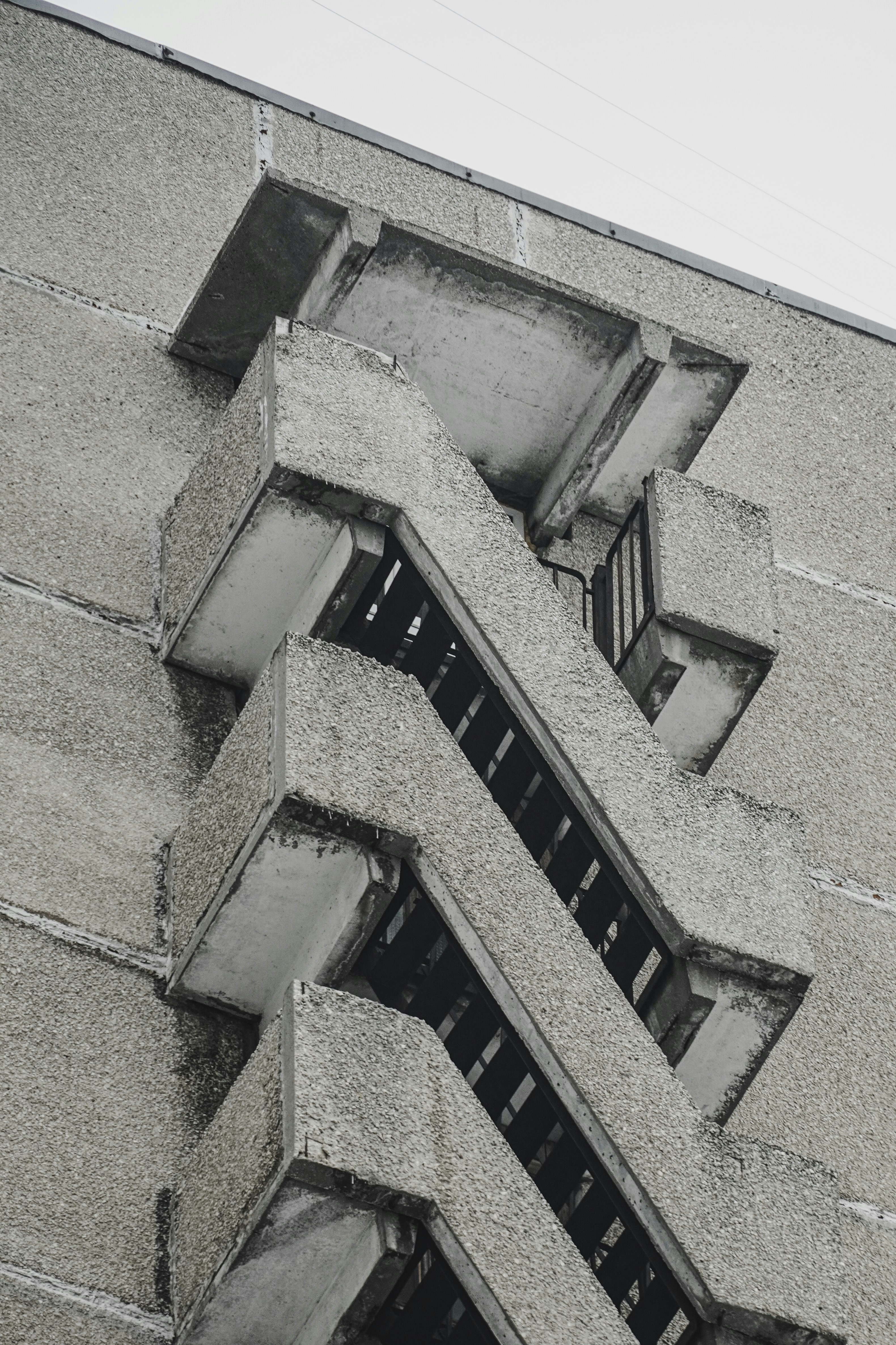 Abstract view of a concrete staircase with zigzag design against a gray wall. The image highlights the structural elements and textures of urban architecture.