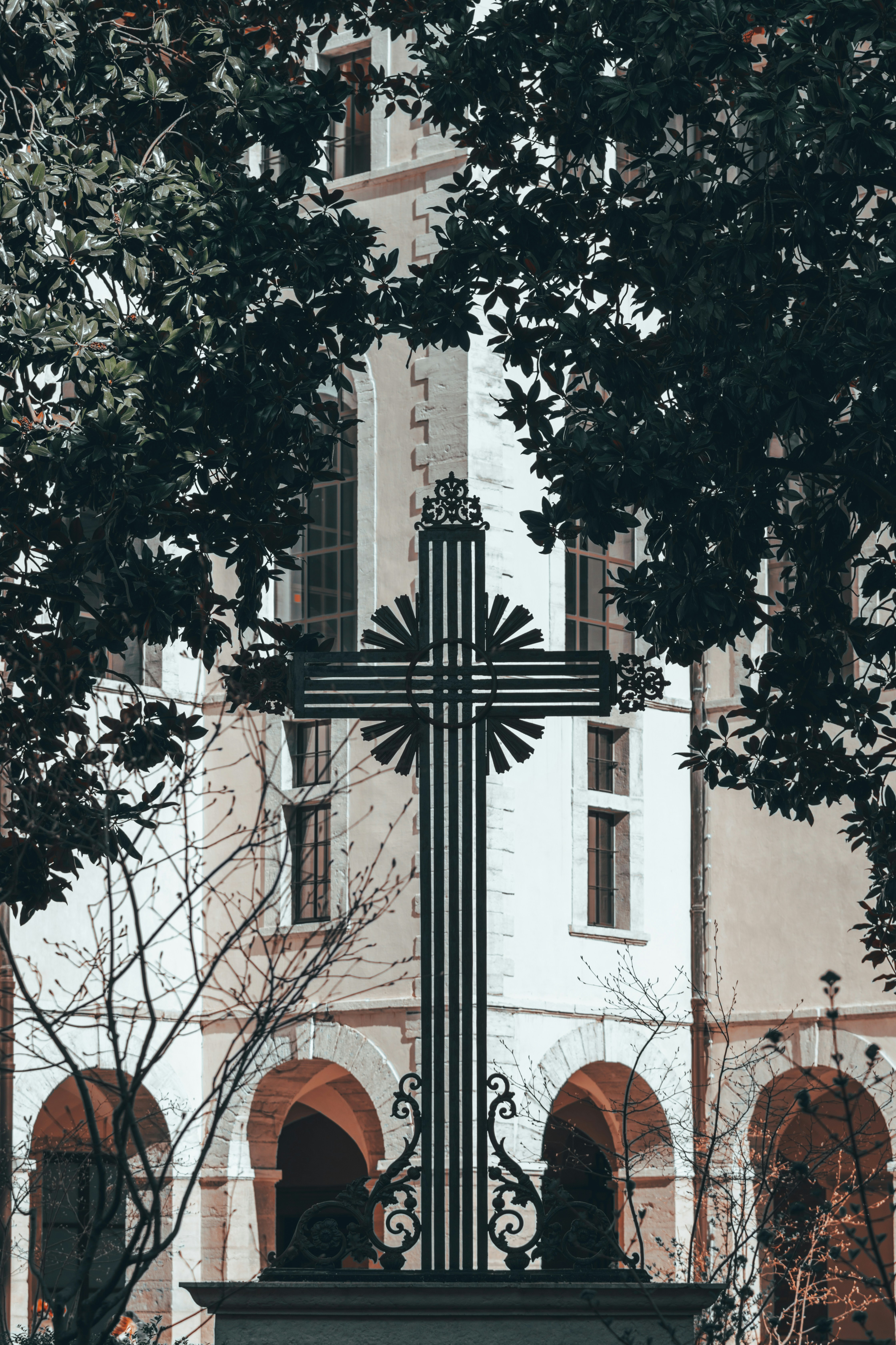 Cross in the Courtyard: Ironwork Framed by Arches and Winter Foliage