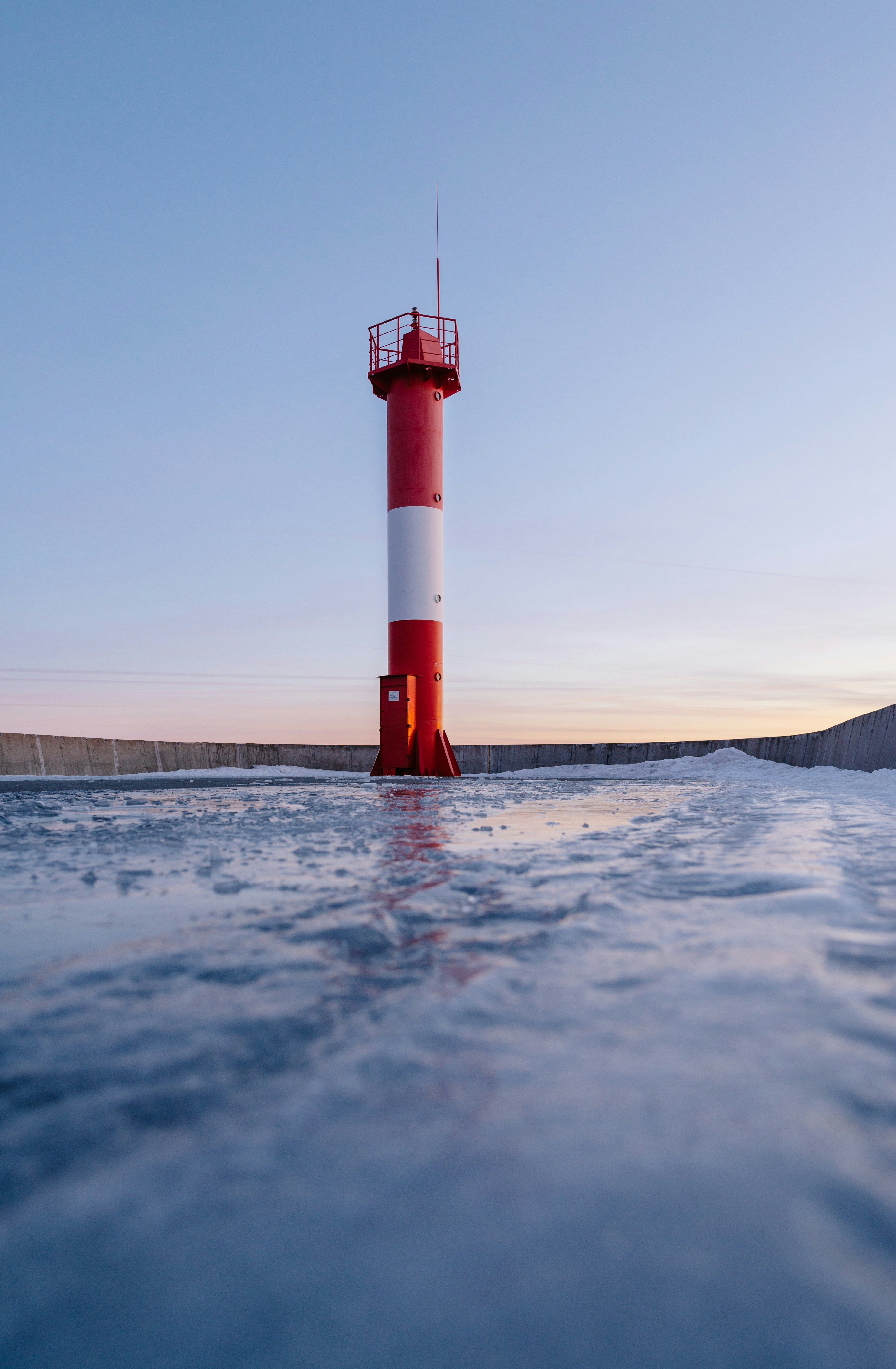 Beacon on Ice: A Red-and-White Lighthouse Piercing the Pale Sunset