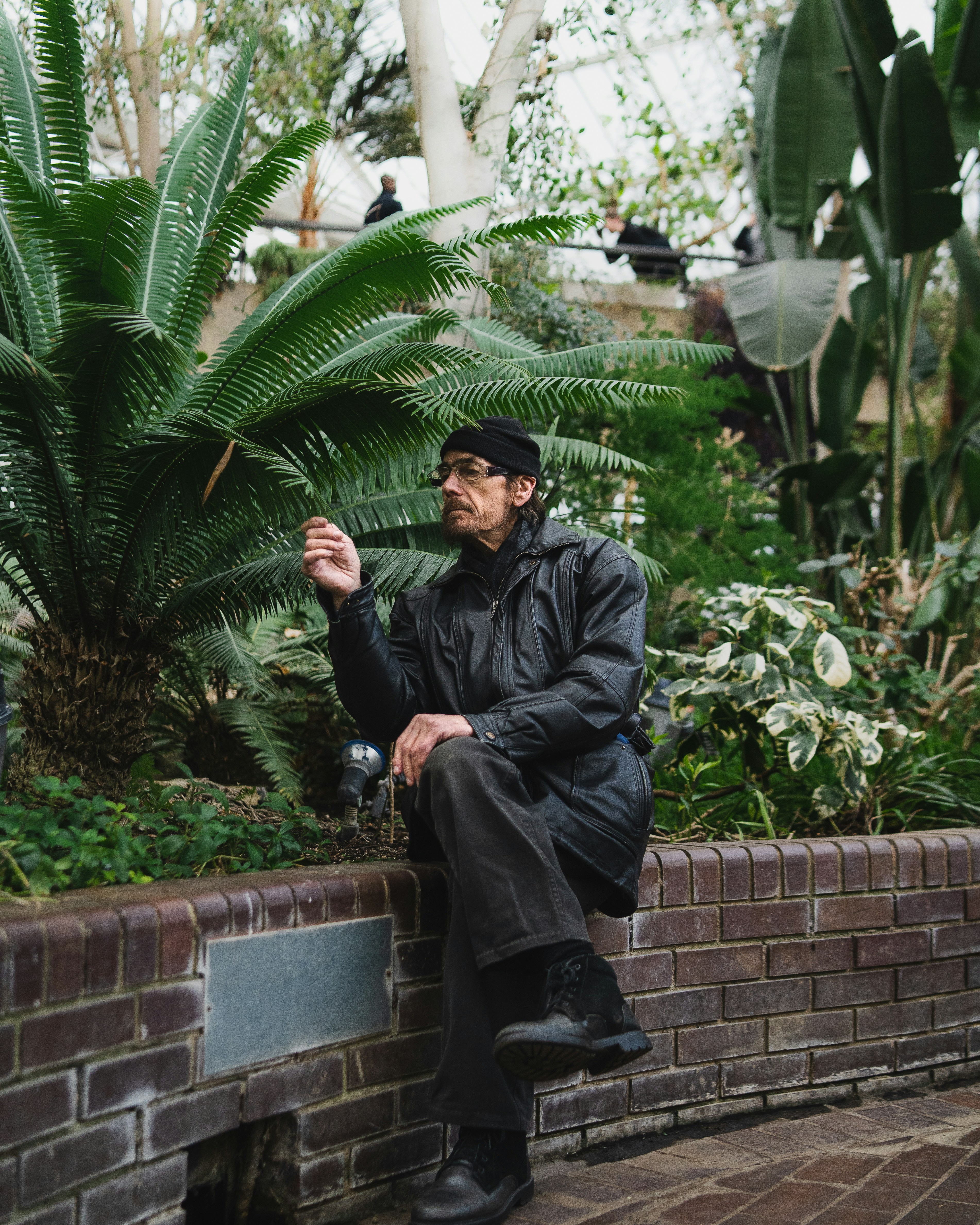 a man sitting on a brick wall next to a plant
