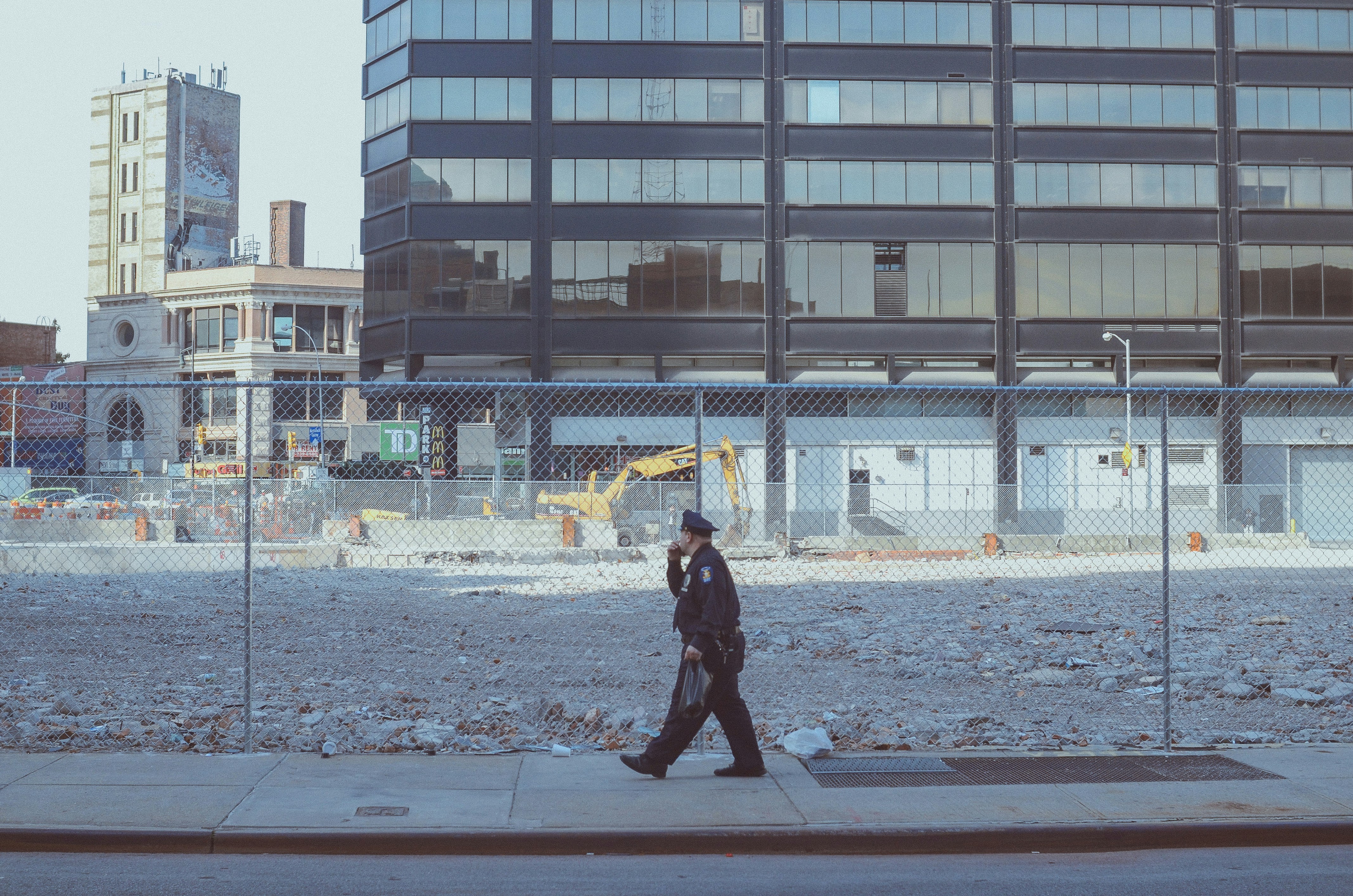 A police officer walking past a construction site in a bustling urban environment, highlighting the contrast between stability and development.