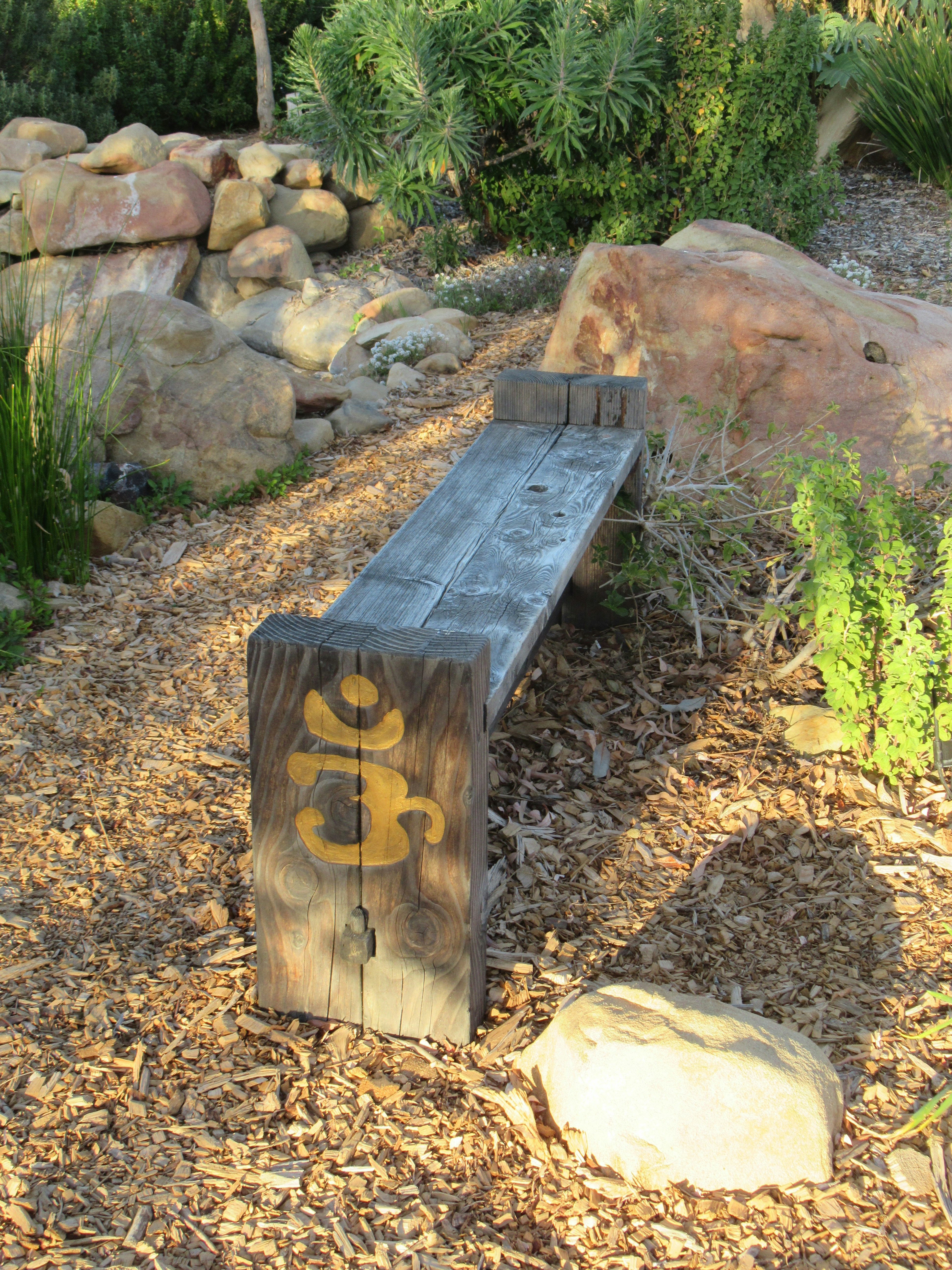 Hindu symbol on wooden bench with rock | a wooden bench sitting in the middle of a garden
