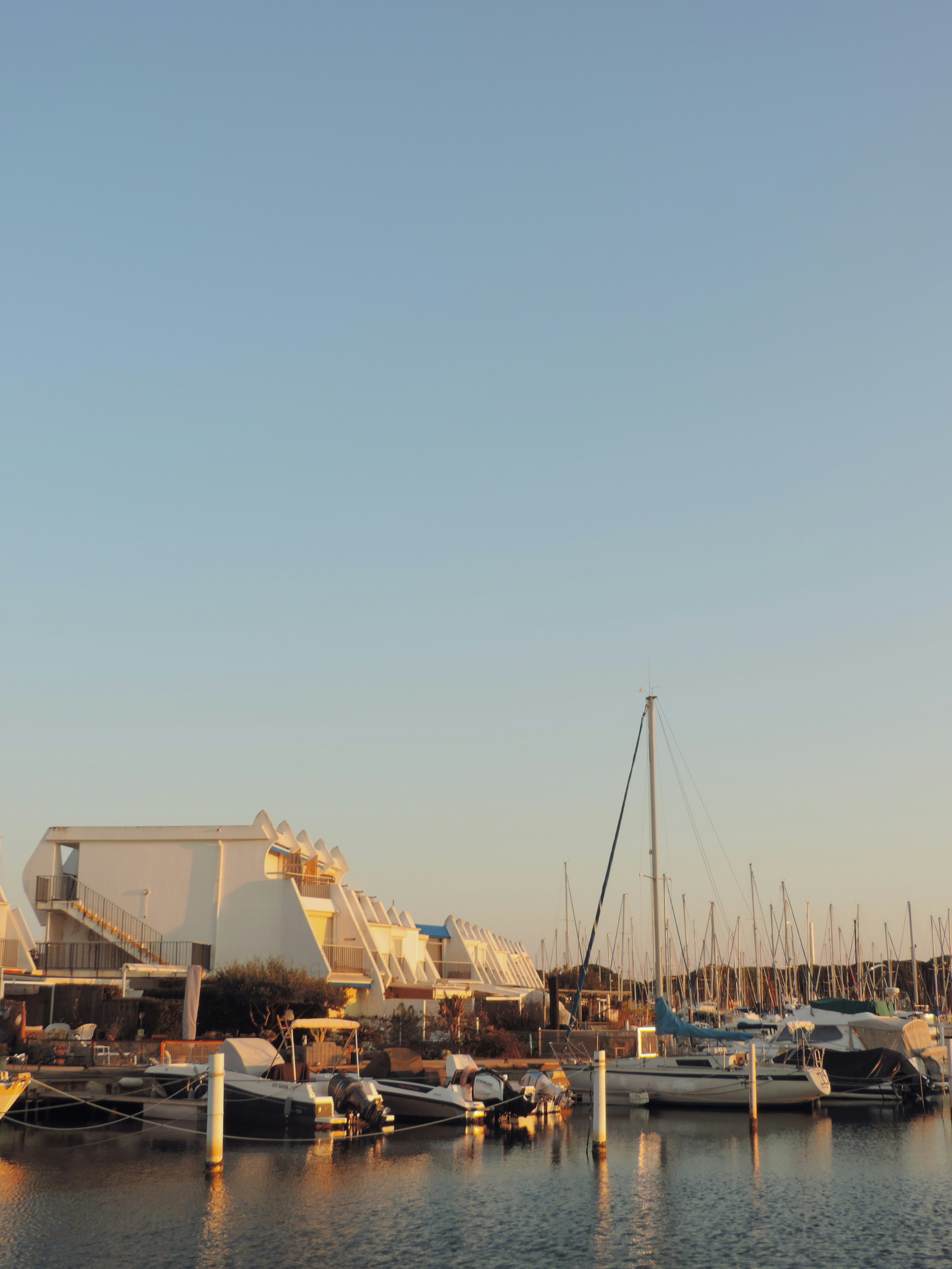 Modern architectural structures line the harbor, with boats gently bobbing in the water under the golden light of dusk.