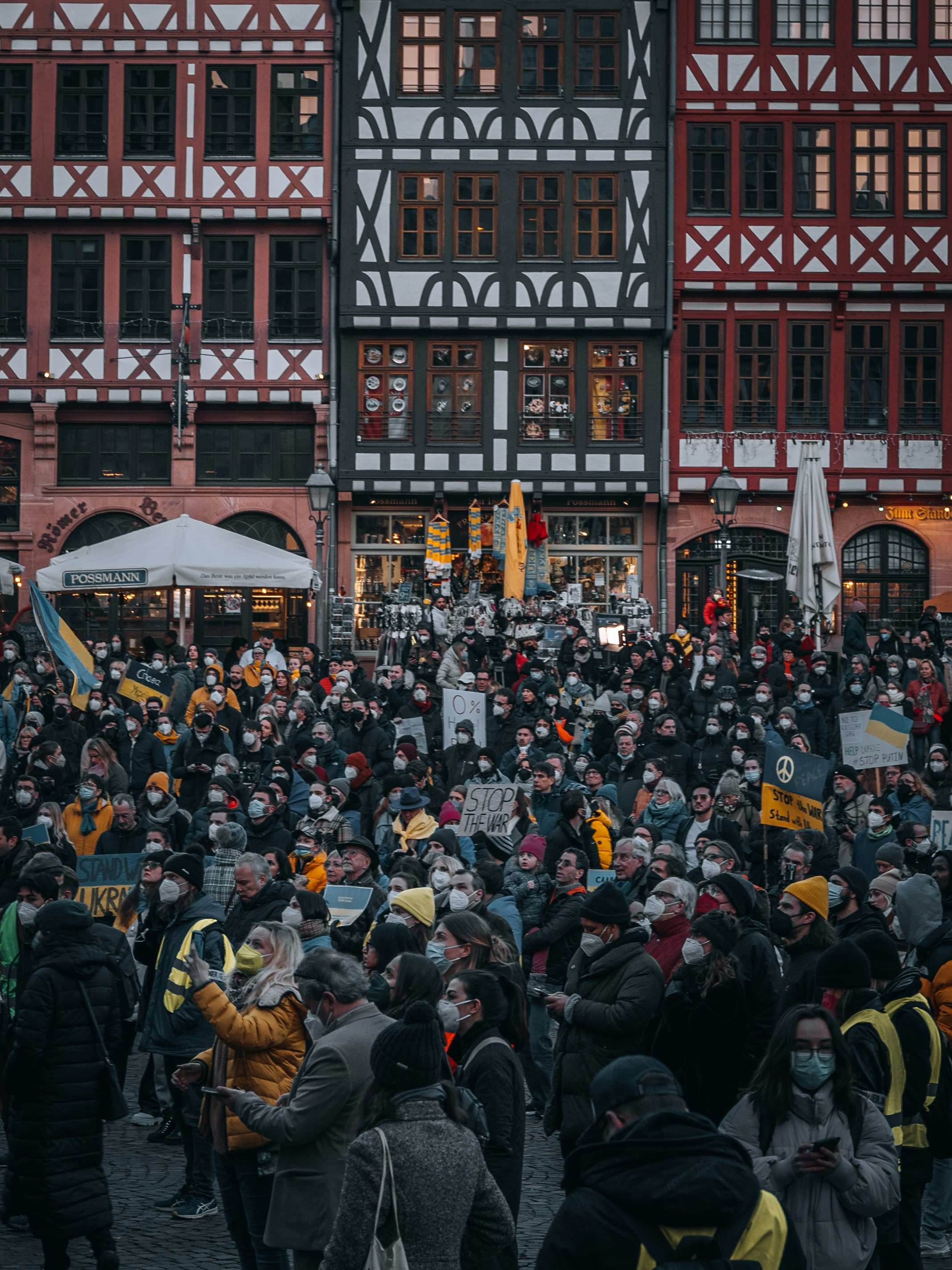 Crowd Protests Beneath Timber-Framed Facades in a European Town Square at Dusk