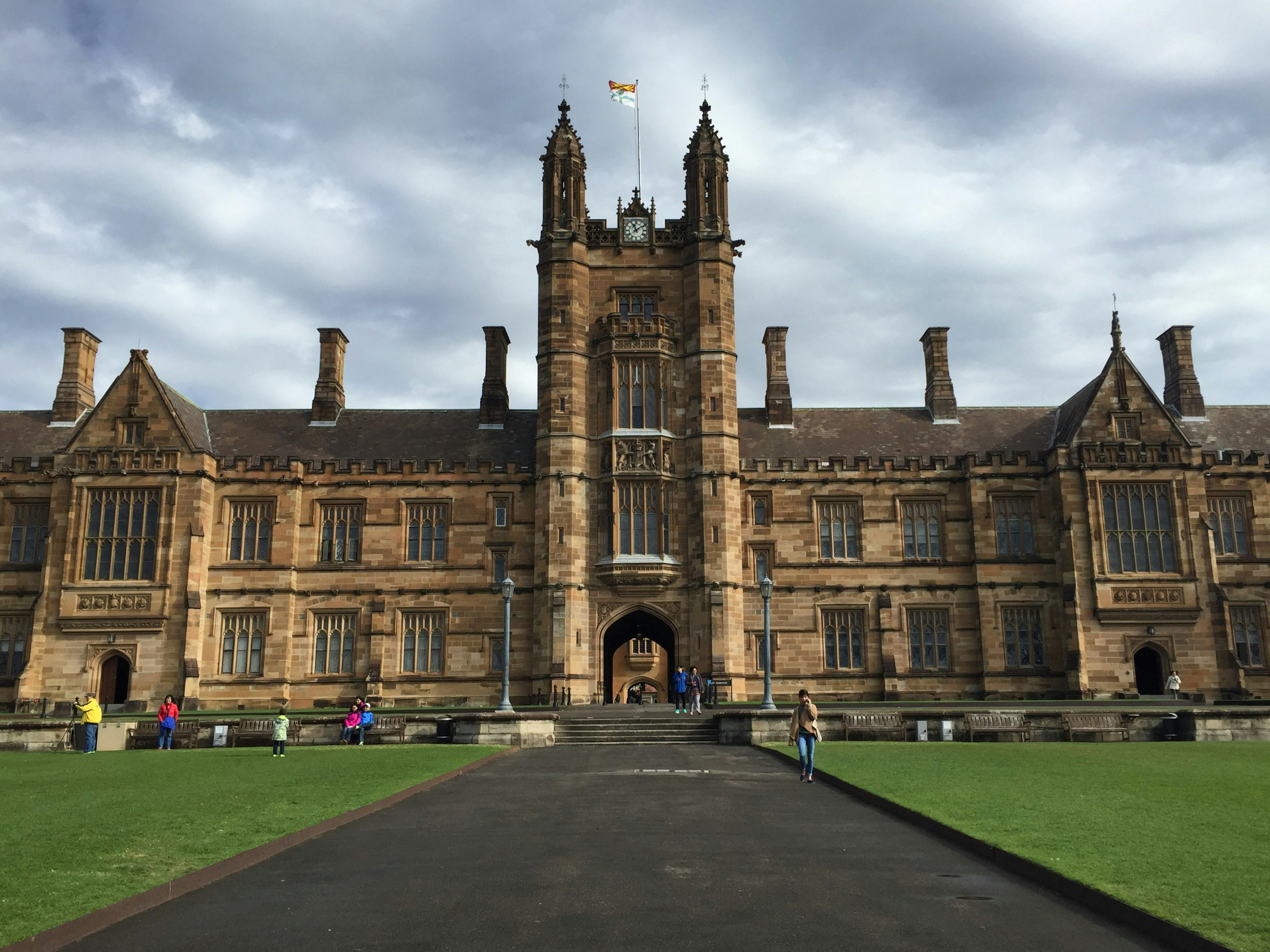 Historic university building showcasing intricate architecture and vibrant campus life with students walking on the pathway.