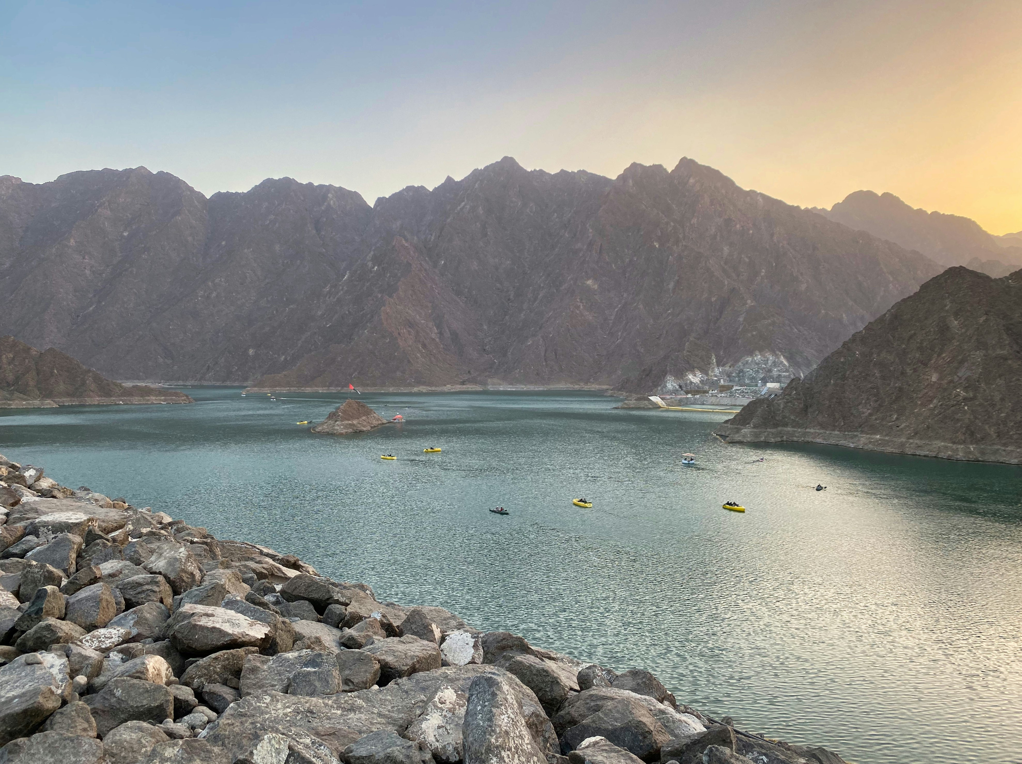 Vast lake surrounded by rugged mountains at sunset, with small boats dotting the water's surface. The tranquil scene evokes a sense of peace and adventure.