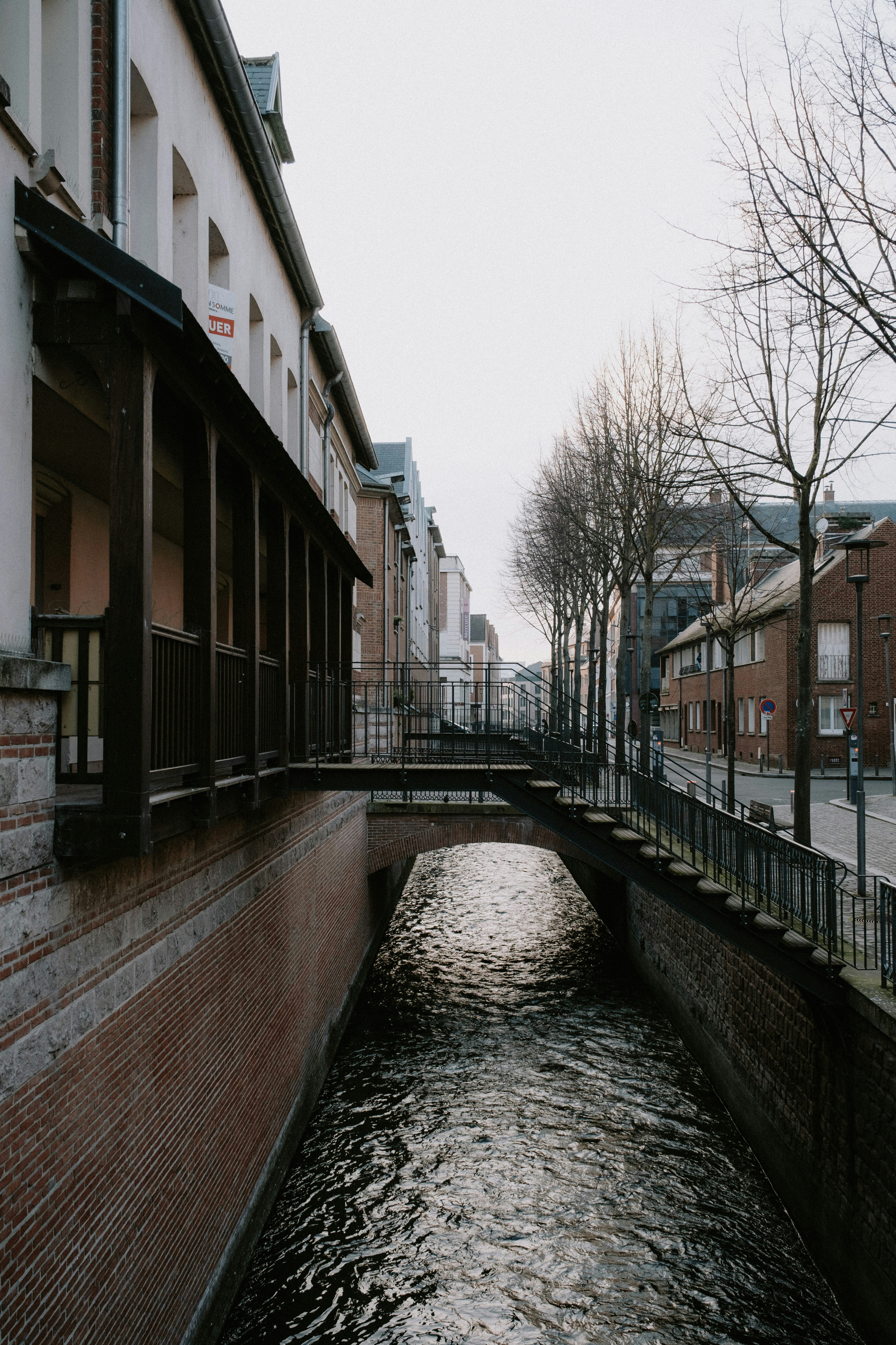 A serene canal flows beneath a quaint bridge, flanked by charming buildings and leafless trees, capturing the essence of urban tranquility.