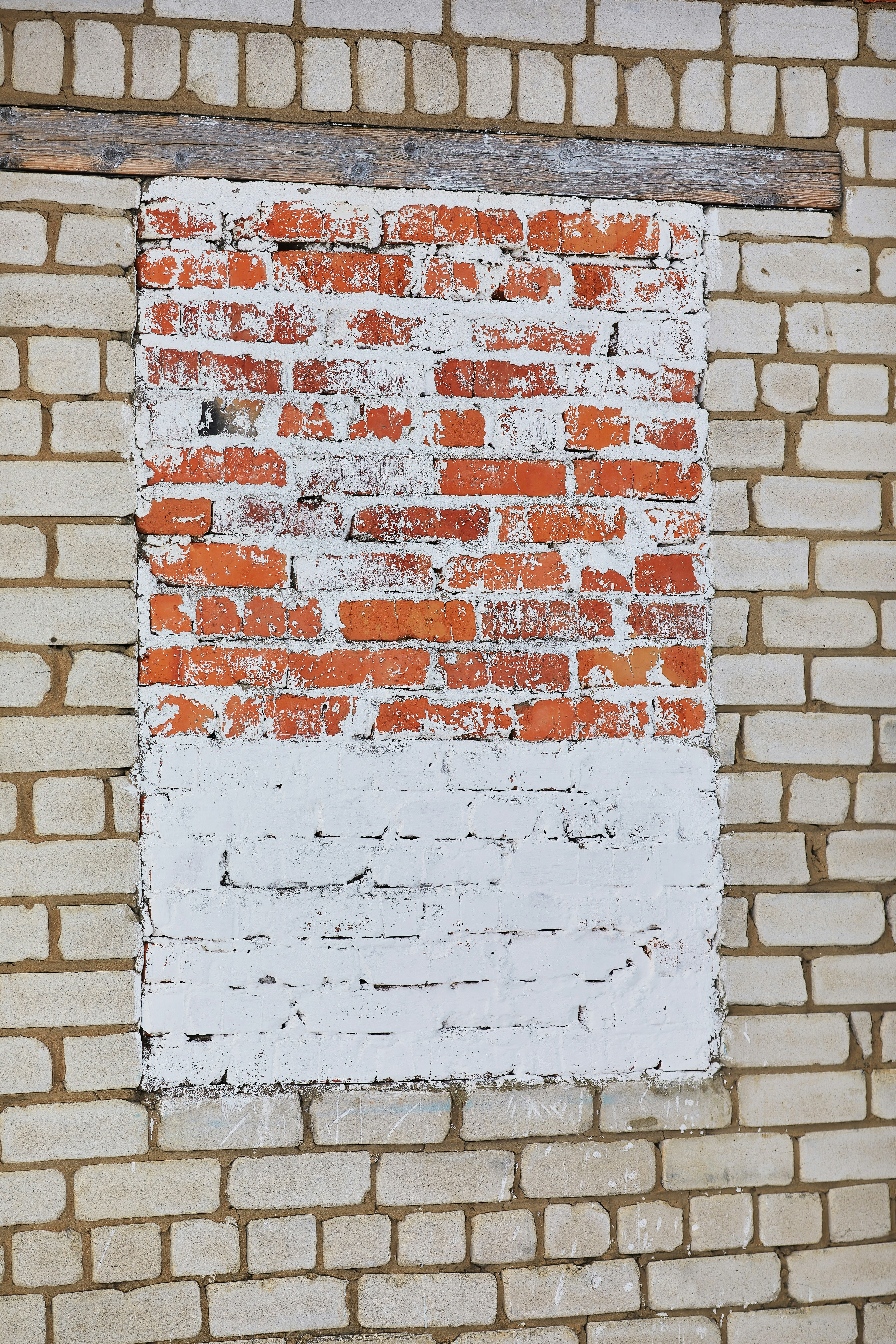 Weathered brick wall with a patch of white paint, revealing layers of history and neglect.