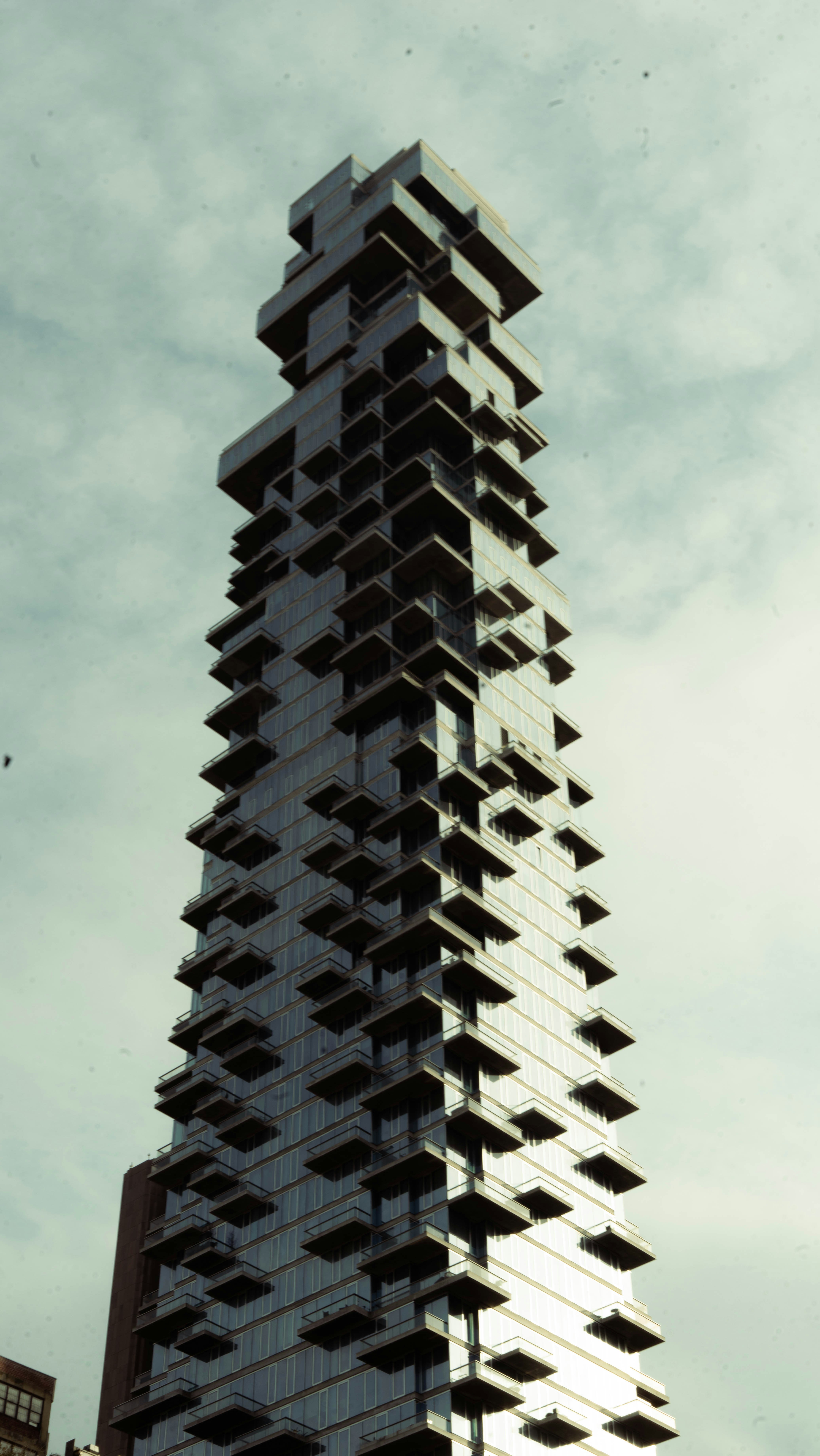 Sleek, modern skyscraper with a unique, staggered design, showcasing a blend of glass and concrete elements against a cloudy sky.