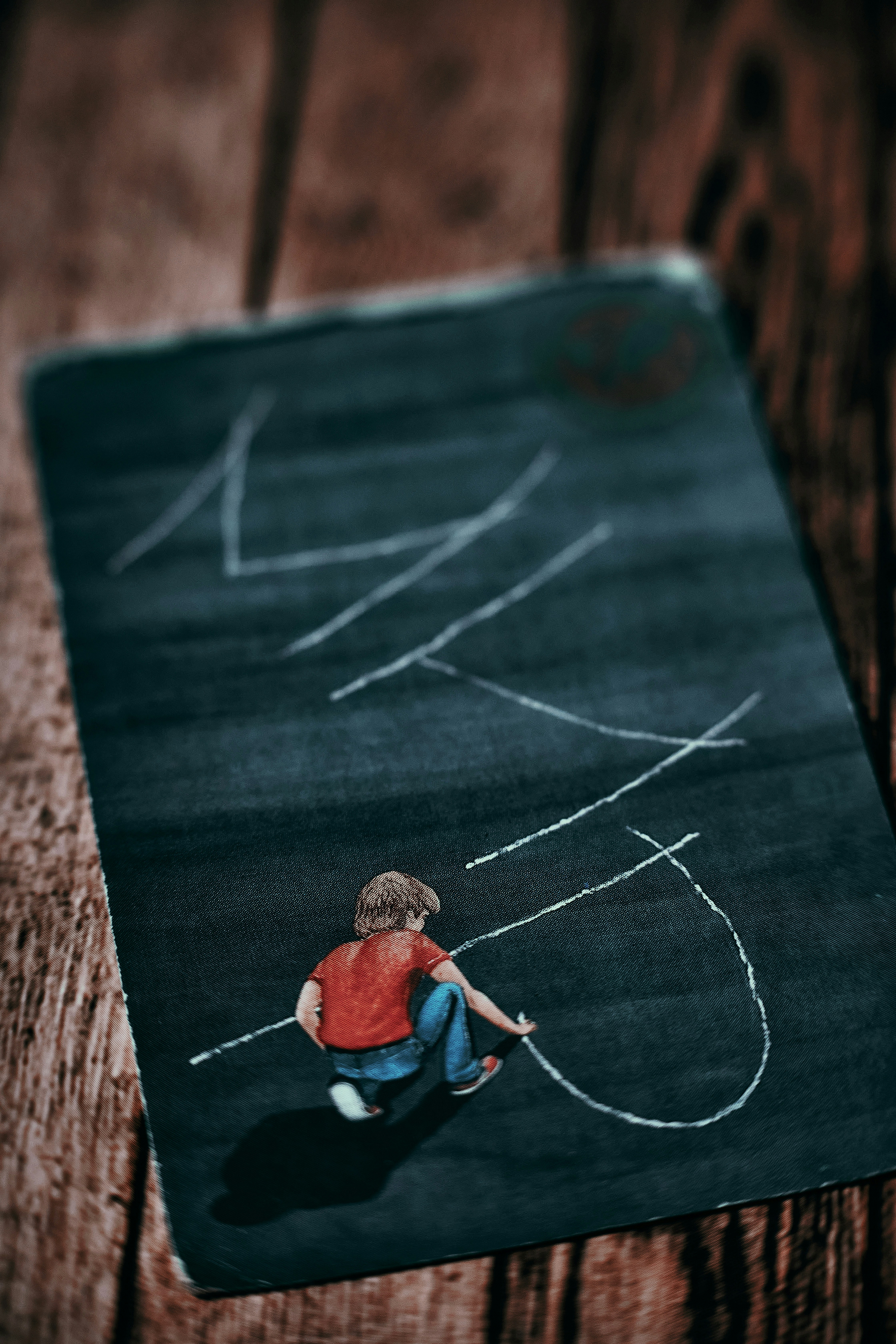 Un jeune garçon assis sur un tableau noir avec de la craie qui écrit ...