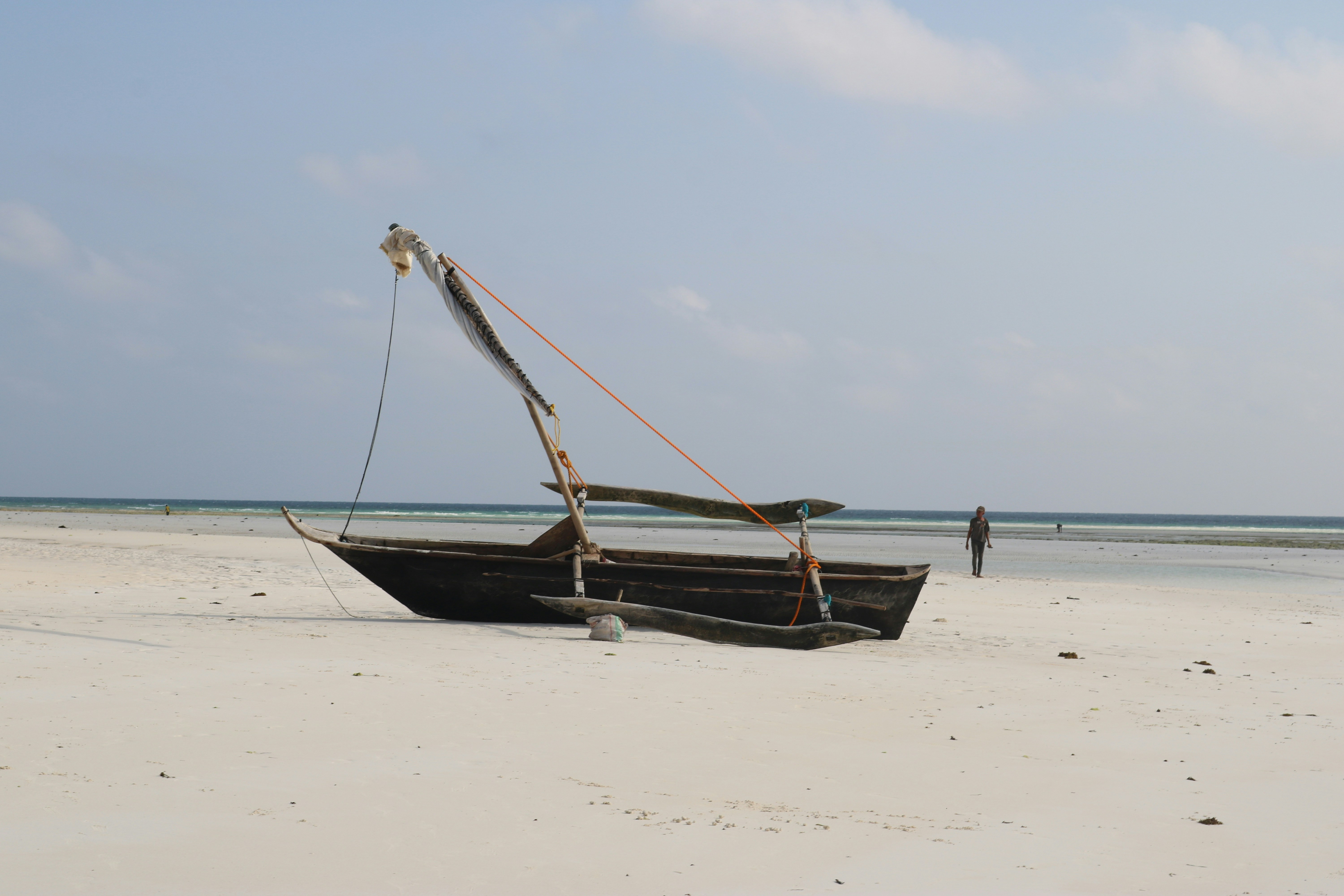 A traditional fishing boat rests on the sandy beach, with a lone figure walking in the distance. The serene coastal landscape evokes a sense of calm.
