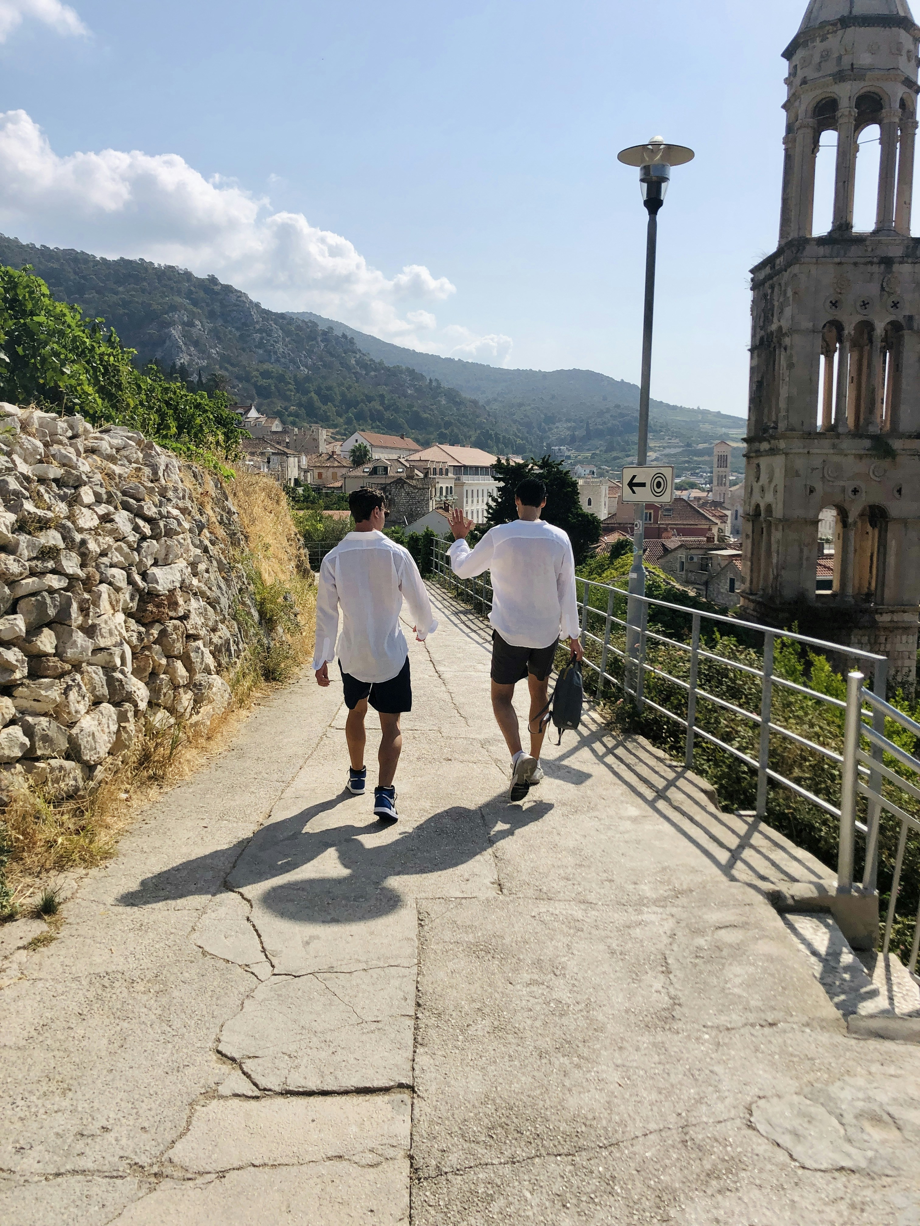 a couple of men walking down a street next to a stone wall