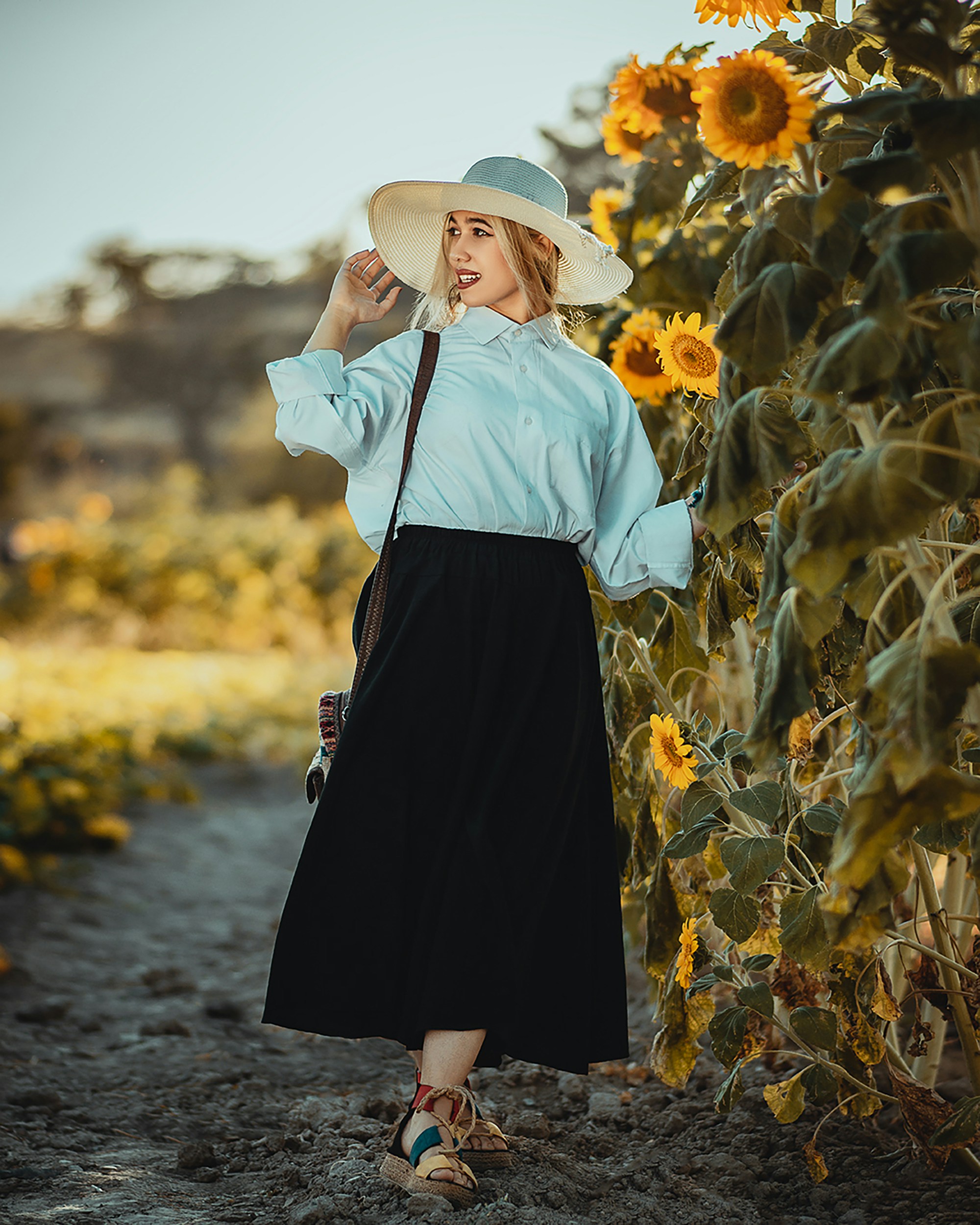 Young woman in a wide-brimmed hat stands among vibrant sunflowers, exuding a sense of joy and tranquility.