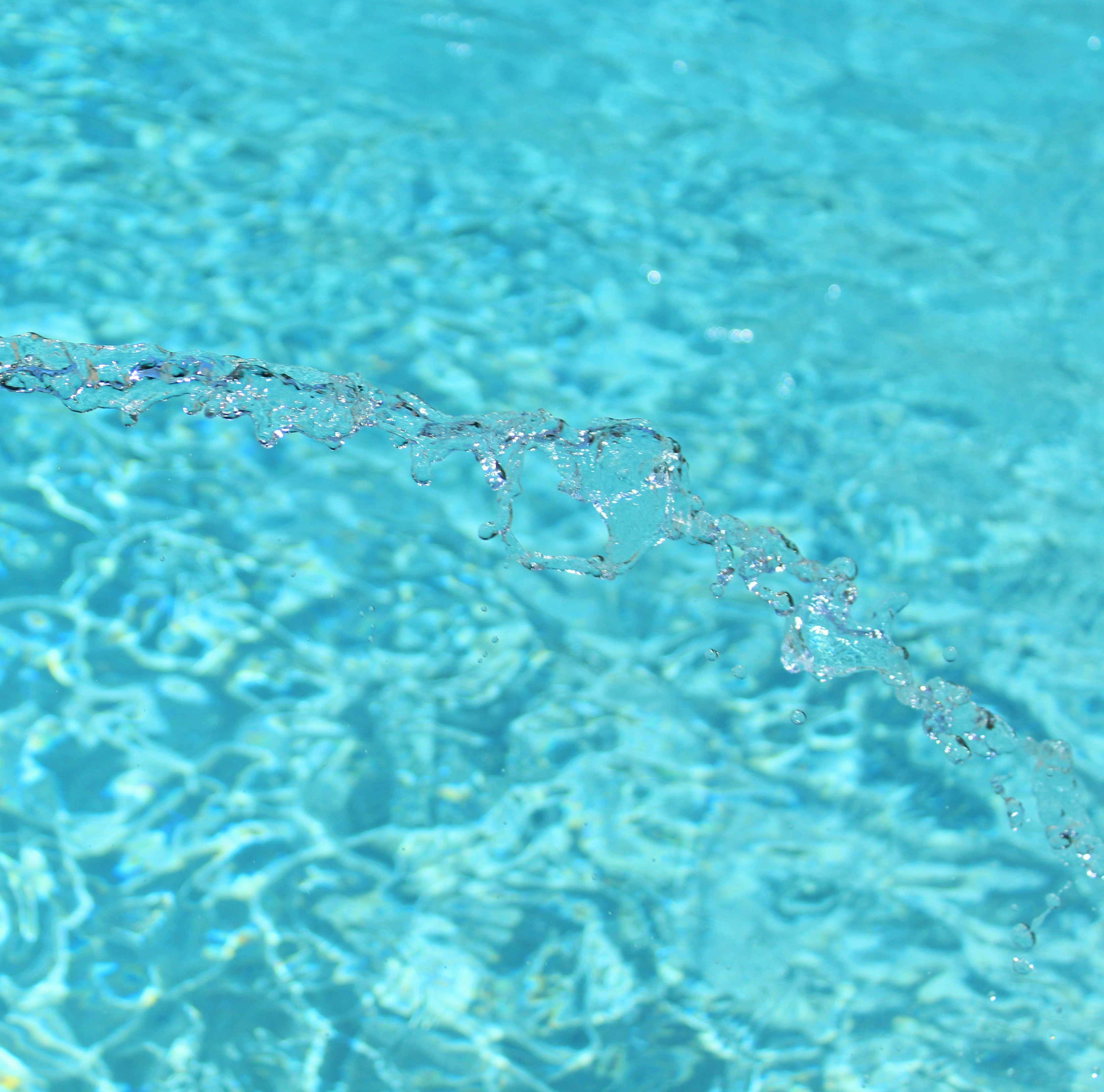 Water gracefully arcs through the air, creating a shimmering trail against a tranquil turquoise backdrop.