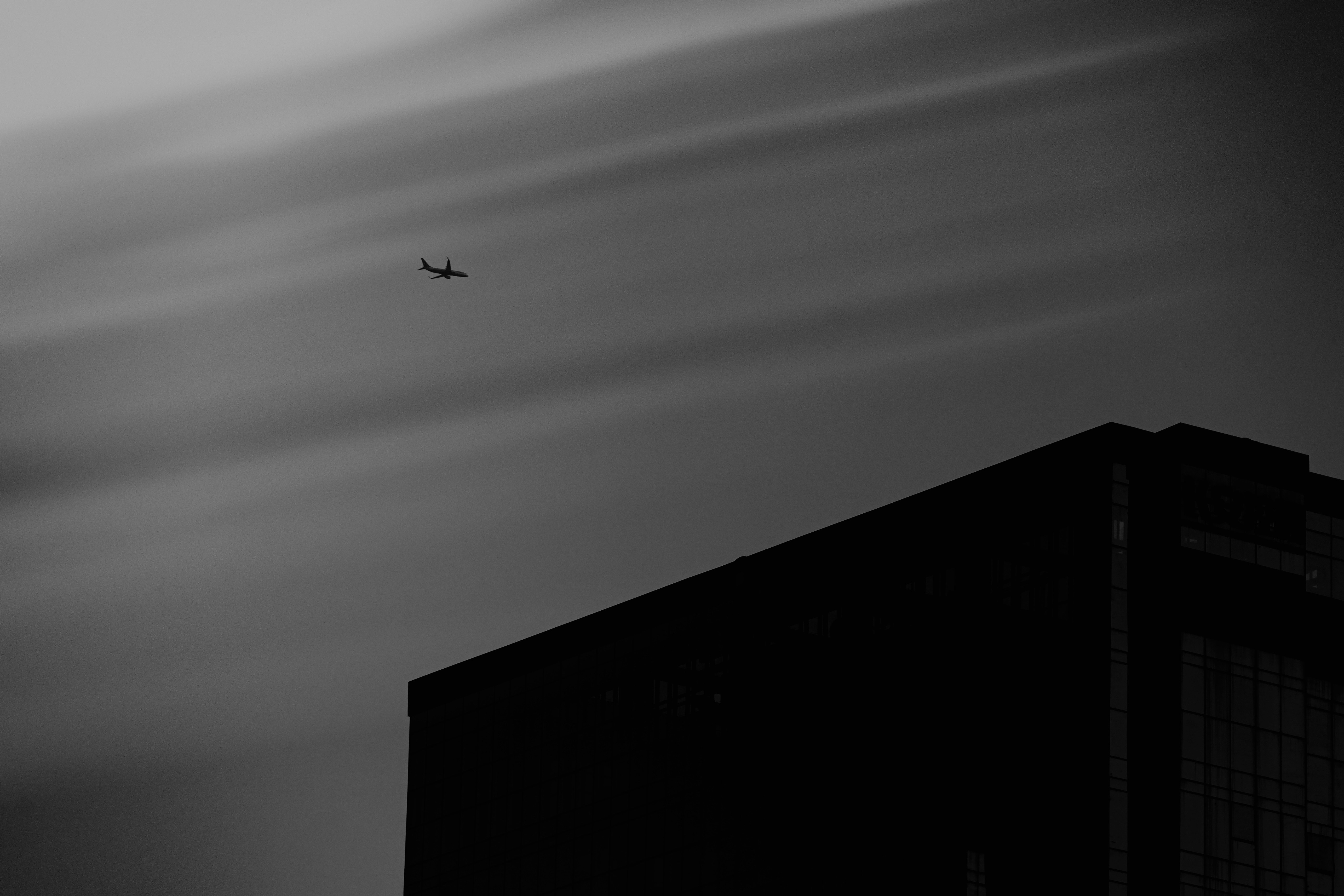 Monochrome hush: A lone plane drifts over a stoic city silhouette