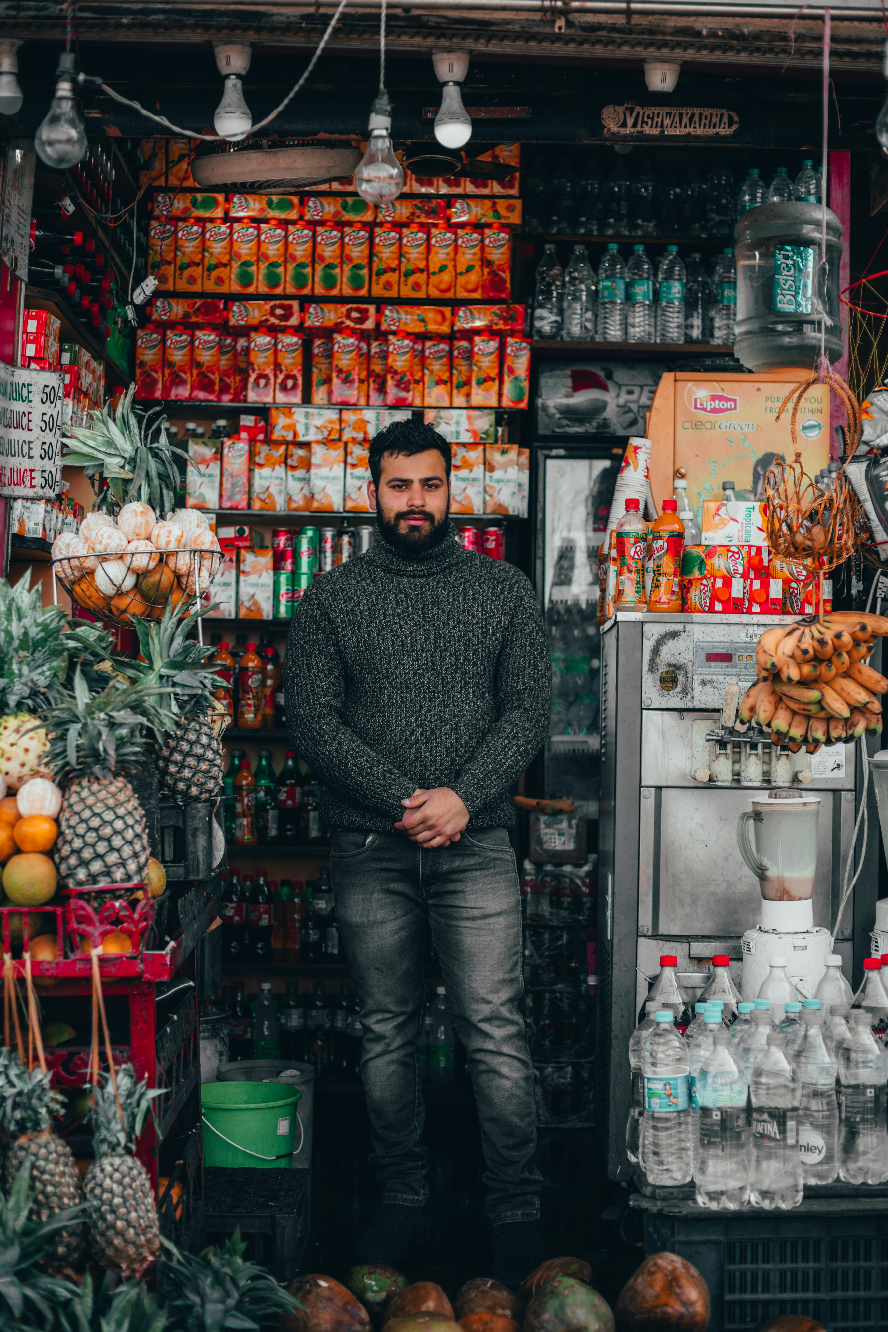 A market vendor stands confidently among a vibrant display of beverages and fresh produce, showcasing the bustling atmosphere of a local shop.