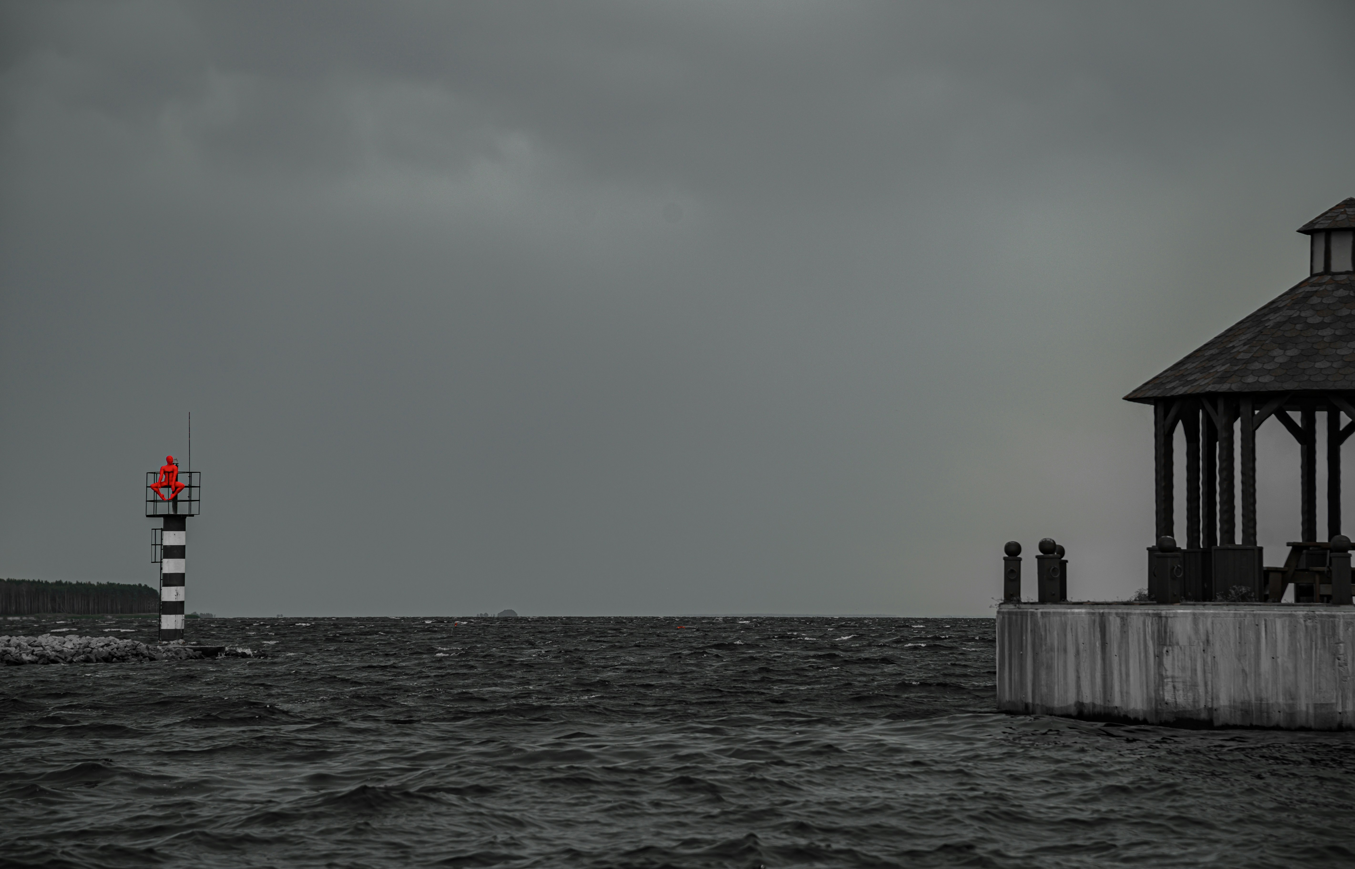 Lighthouse with red light standing tall against dark, turbulent waters under a cloudy sky. The contrasting colors highlight the lighthouse's significance.