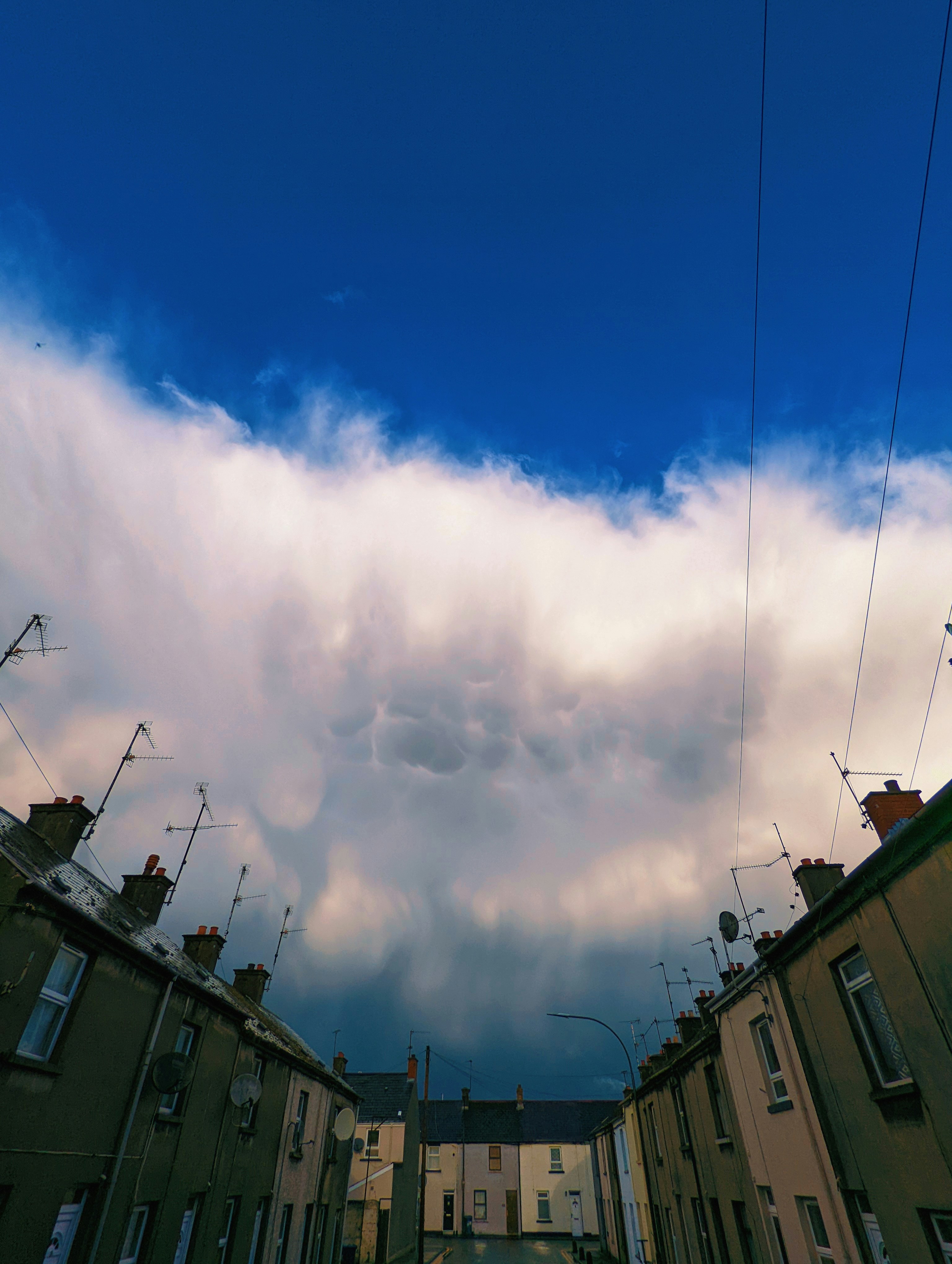Dramatic cloud formation looming over a row of houses, hinting at an impending weather change. The interplay of light and shadow creates a striking atmosphere.