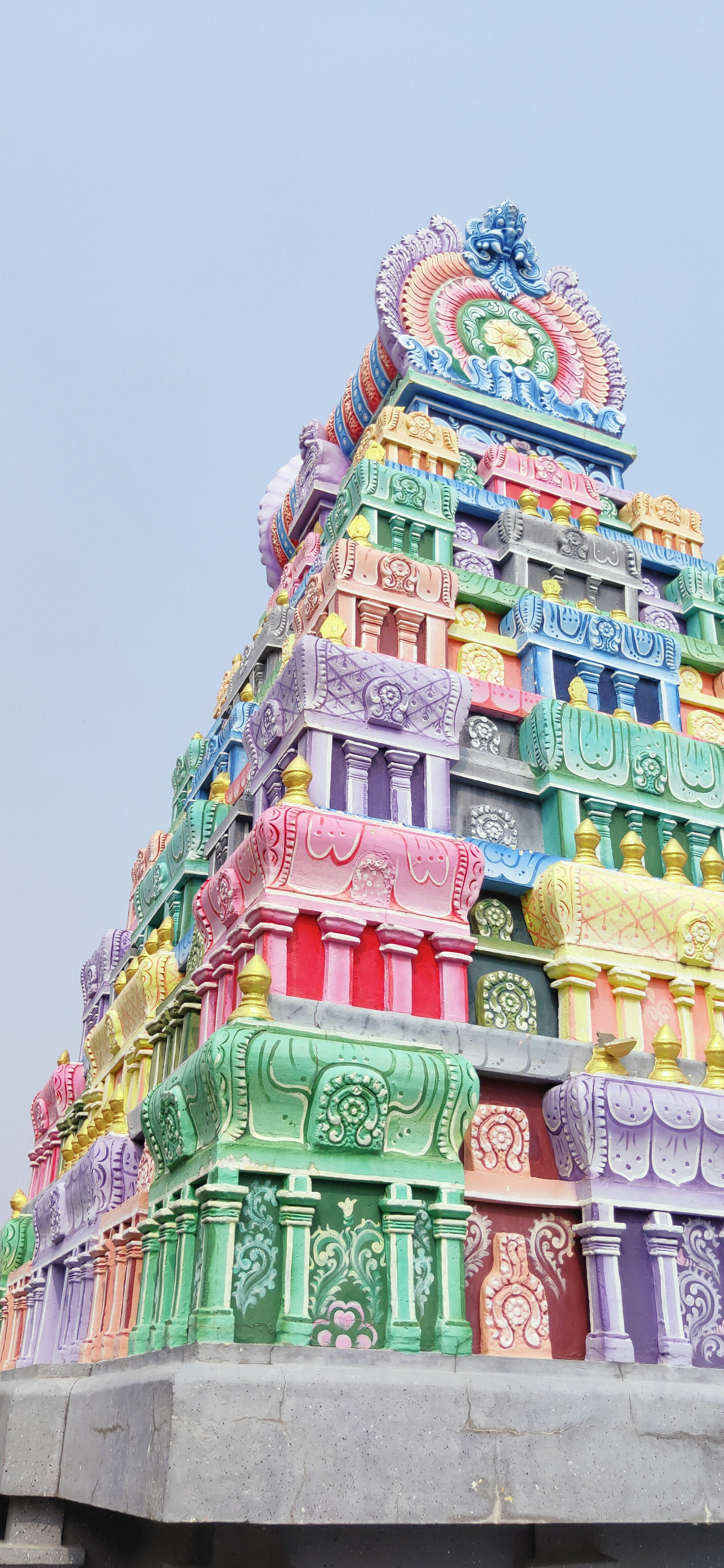 Colorful tiered temple tower with intricate carvings rising against a clear blue sky.