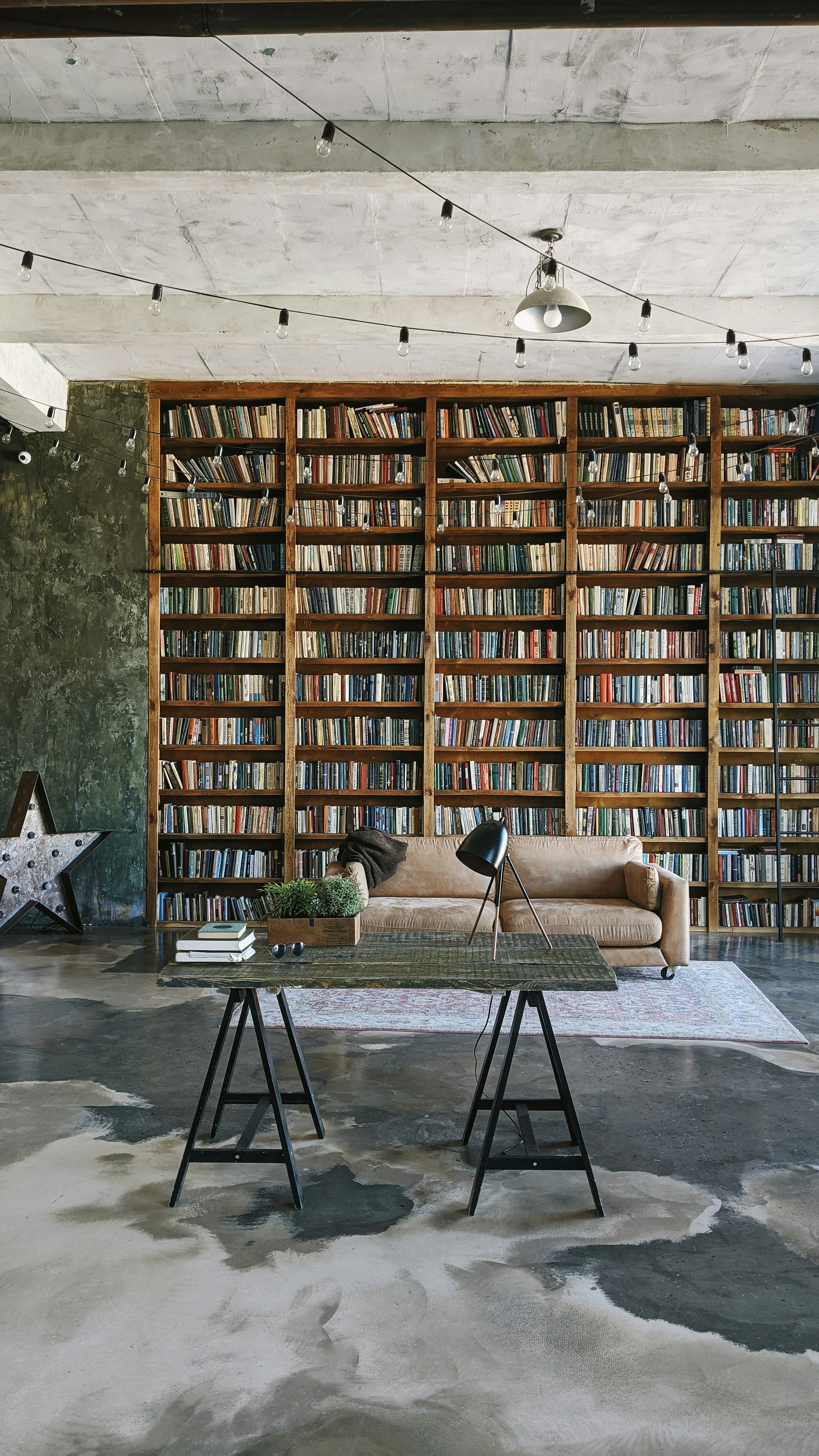 Modern workspace featuring a sleek desk, stylish lamp, and a cozy couch, set against a backdrop of a towering bookshelf filled with books.