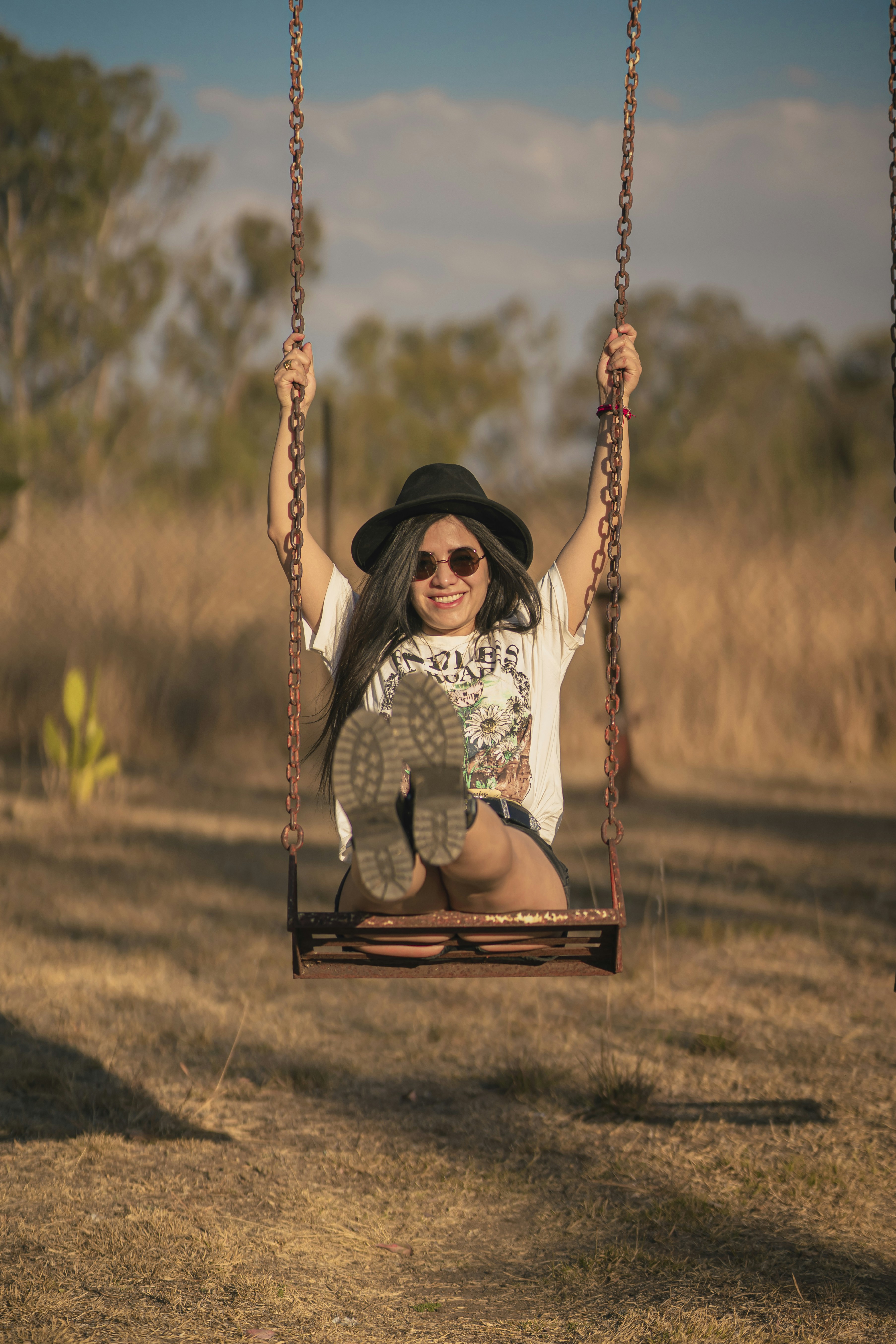 Person relaxing on a swing in a sunlit, grassy field with trees in the background.