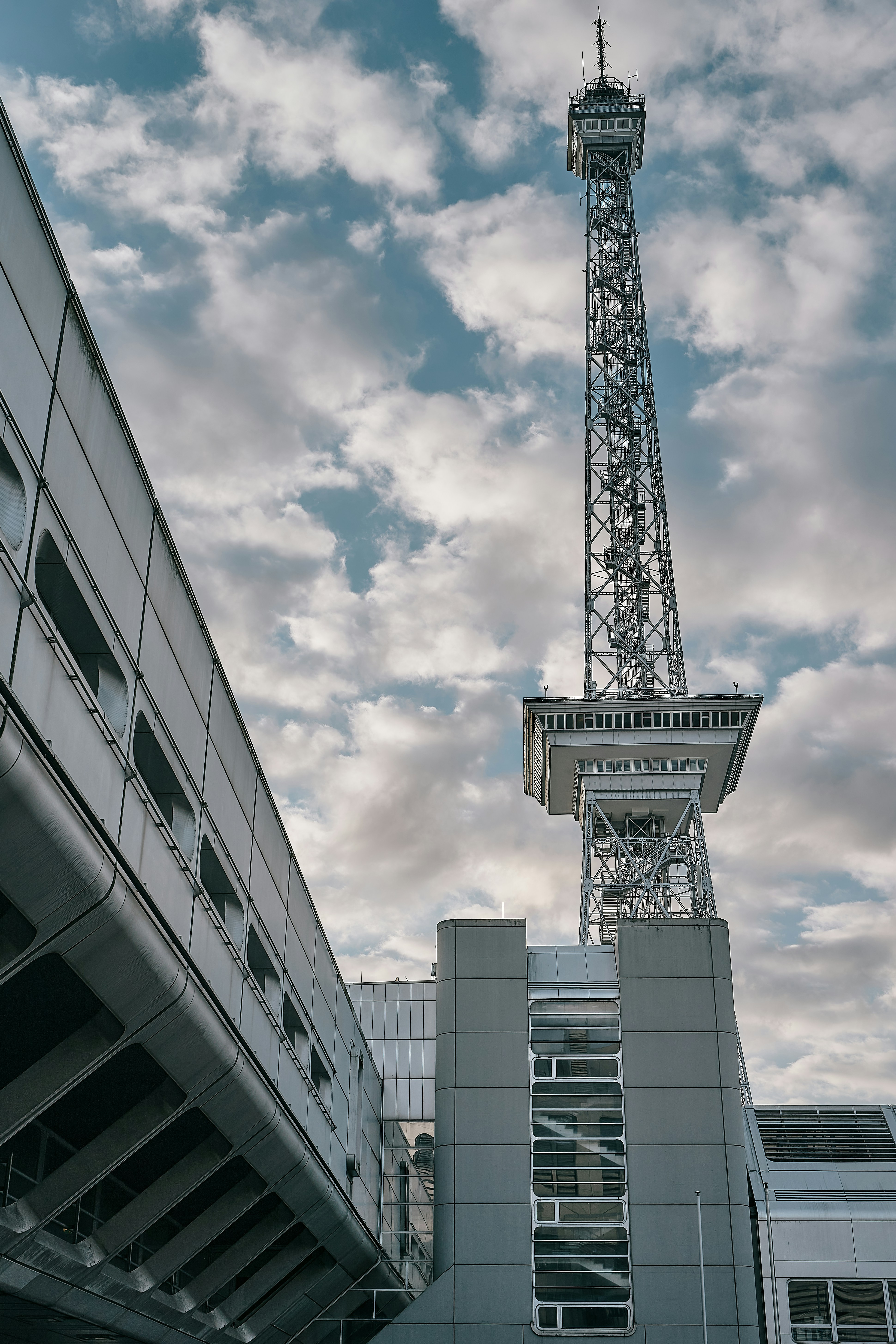 A modern tower rises above a sleek architectural structure under a dynamic sky, showcasing contemporary design elements. The contrast between the tower and the building emphasizes urban innovation.