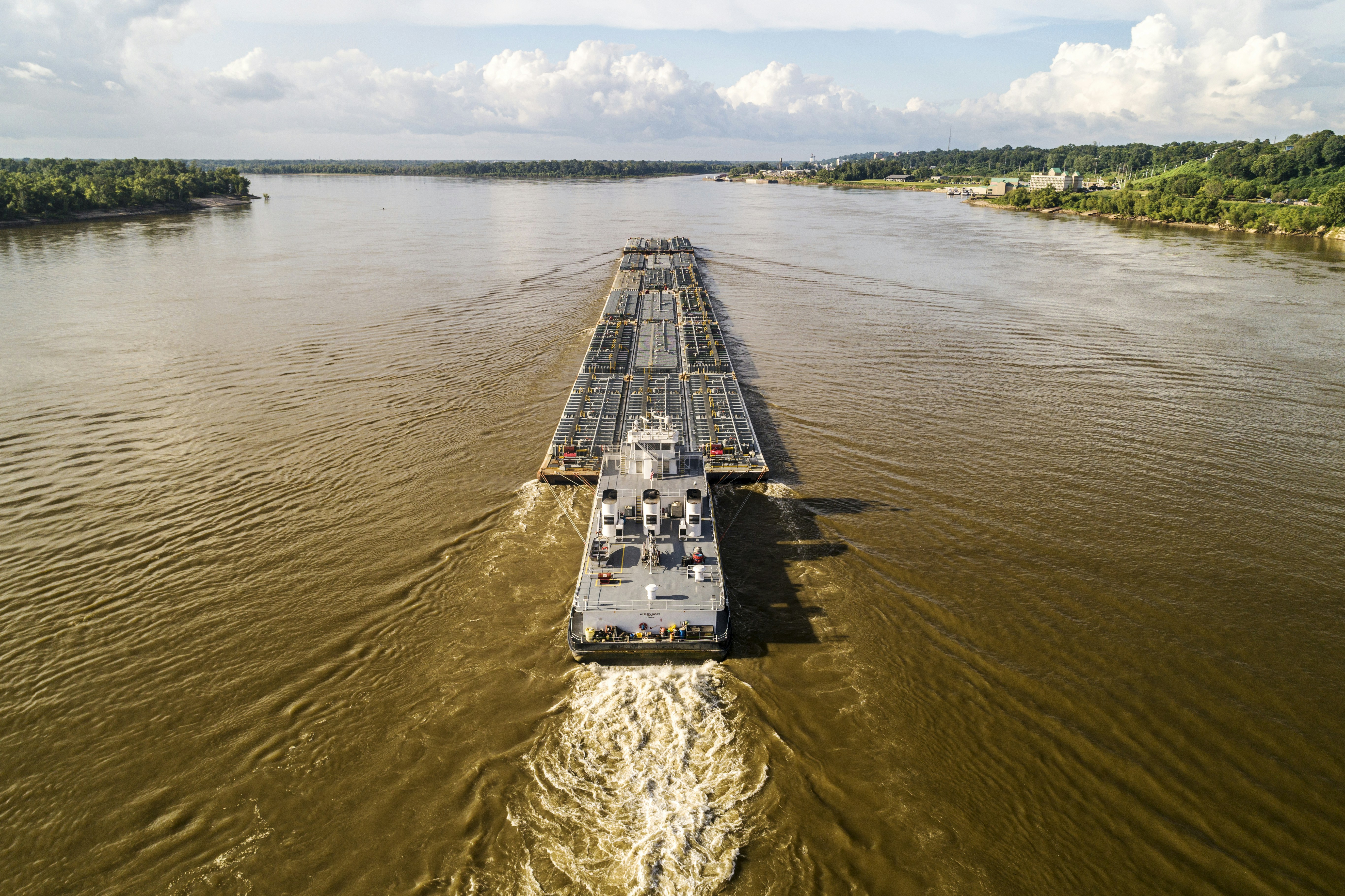 A large barge traveling down a river next to a forest photo – Free ...