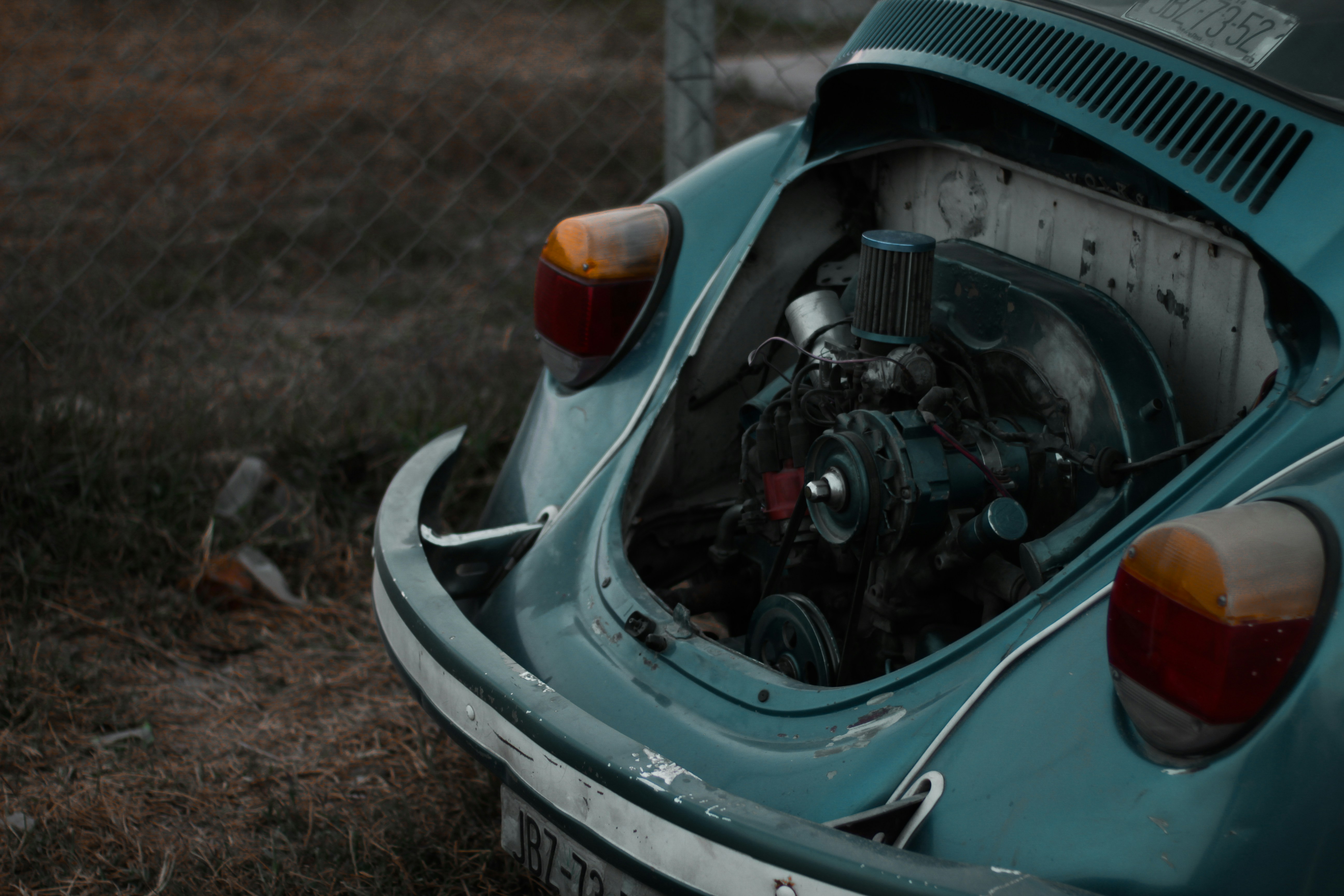 Rear view of a classic blue Volkswagen Beetle with its engine bay open, set against a dimly lit backdrop.