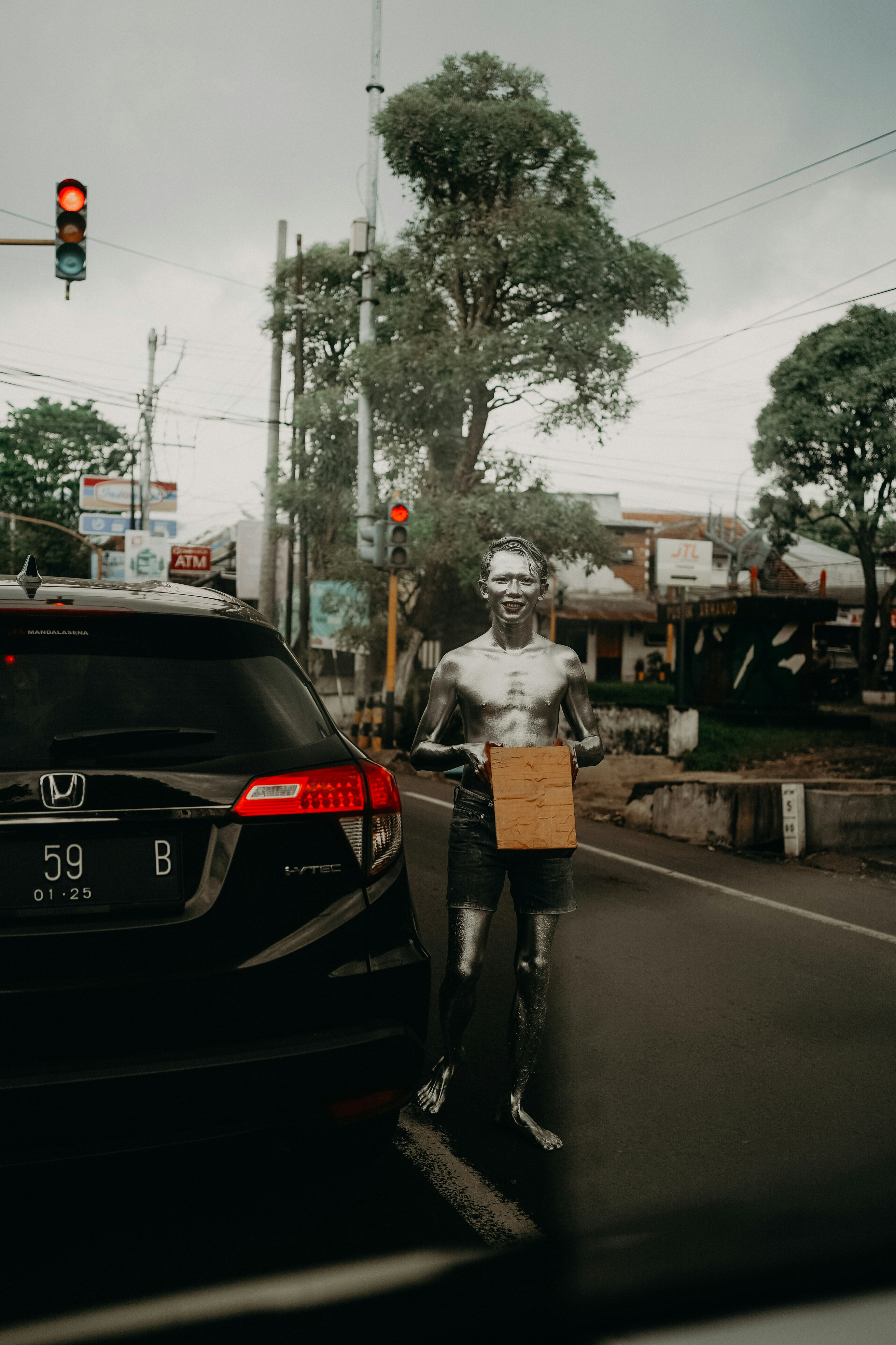 Body-painted street performer with cardboard placard beside a moving car at an urban intersection