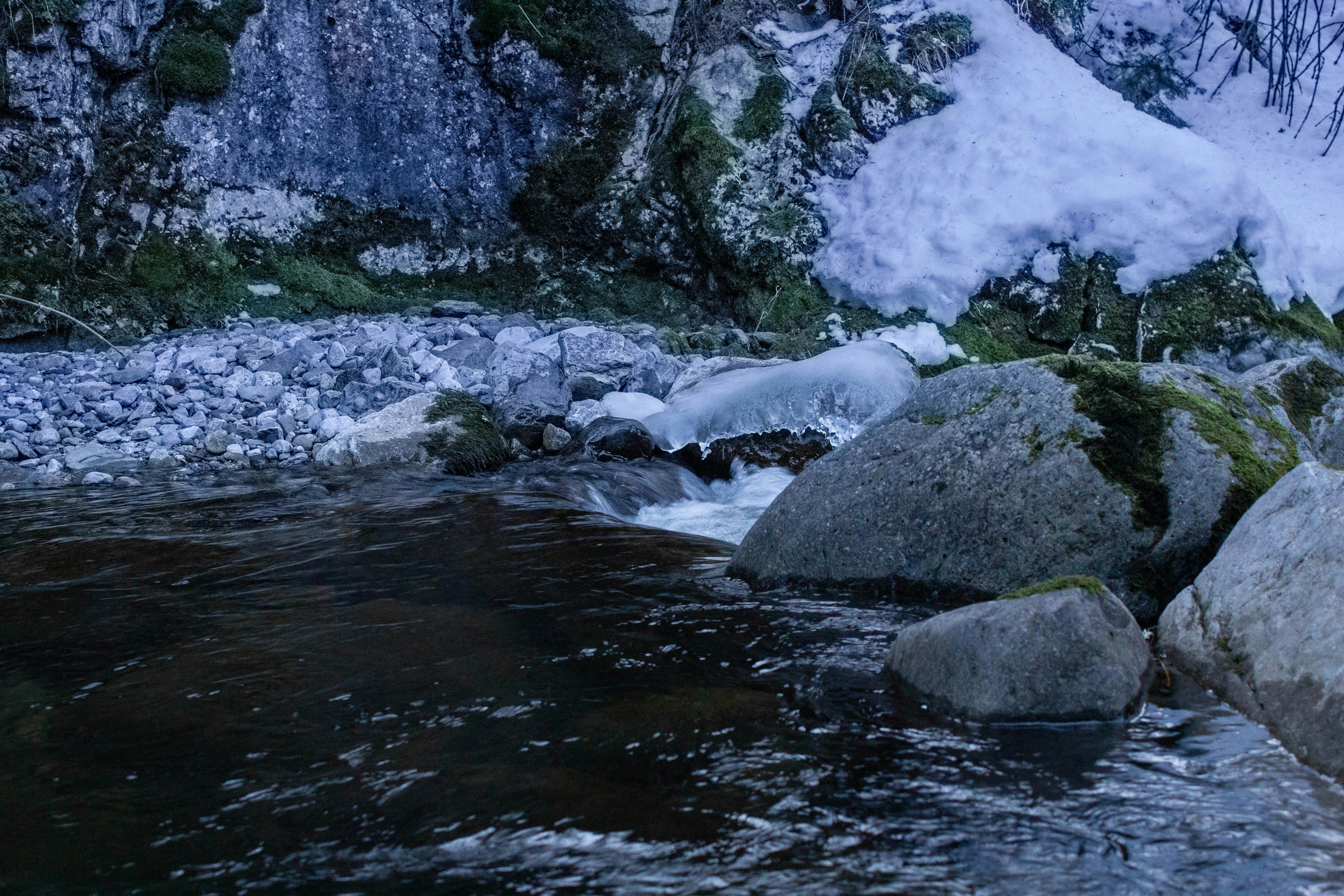 Winter Quiet by the River: Snow-Kissed Stones and Dark Water