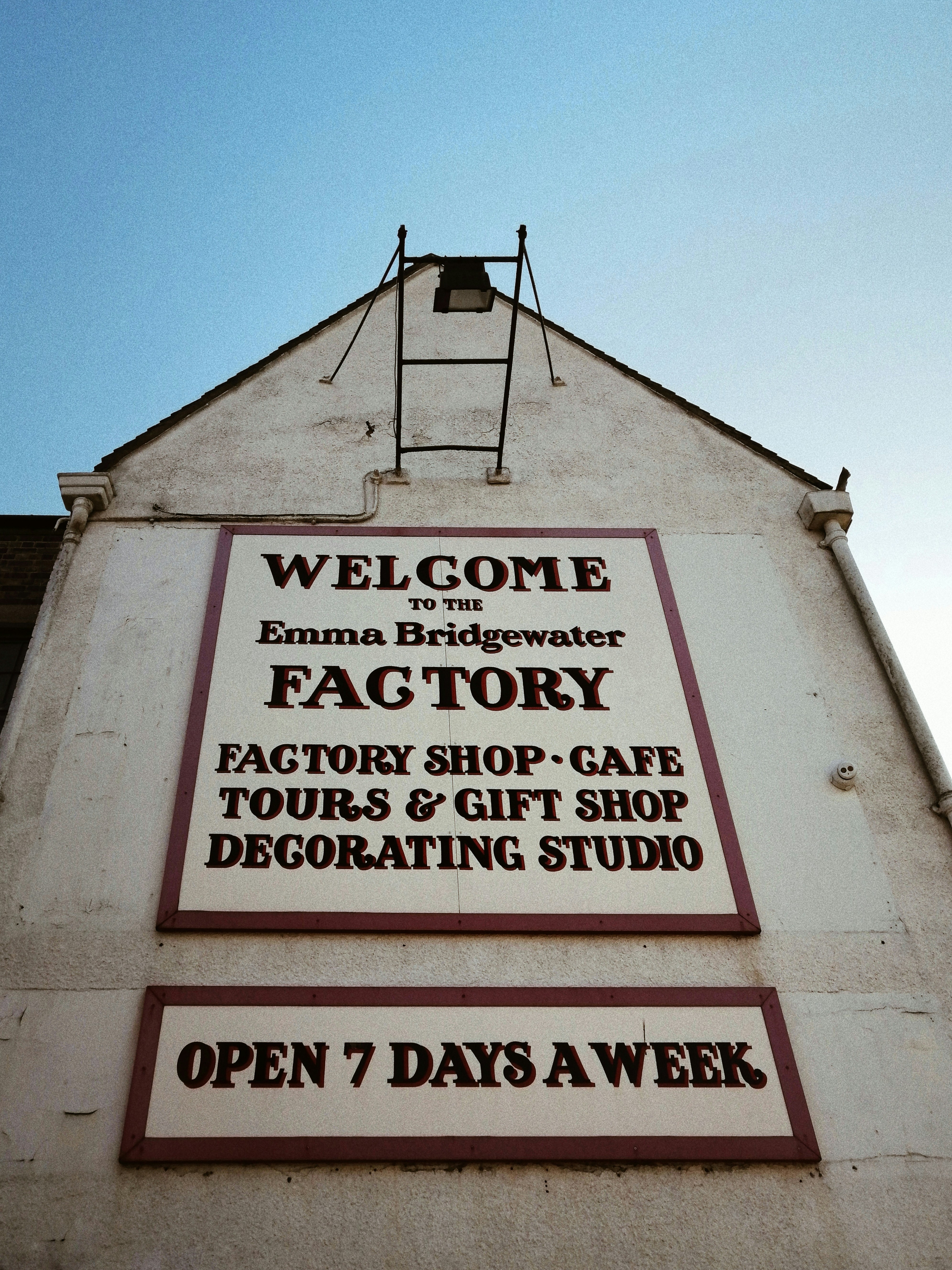 Signage welcoming visitors to the Emma Bridgewater Factory, highlighting various services and offerings. The structure's architecture complements the inviting message.