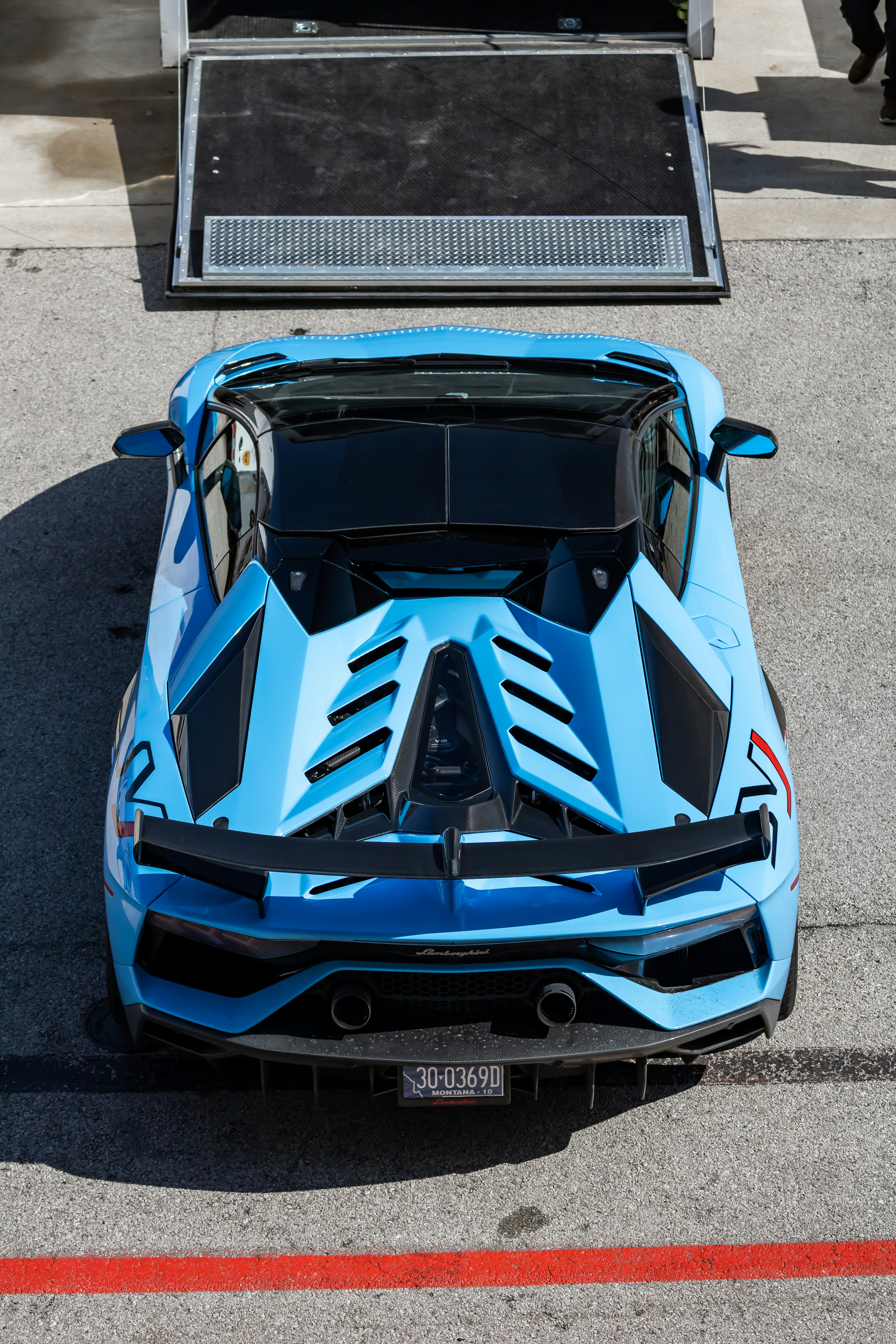 Top-Down Velocity: Blue Sportscar Resting on Asphalt by a Loading Ramp