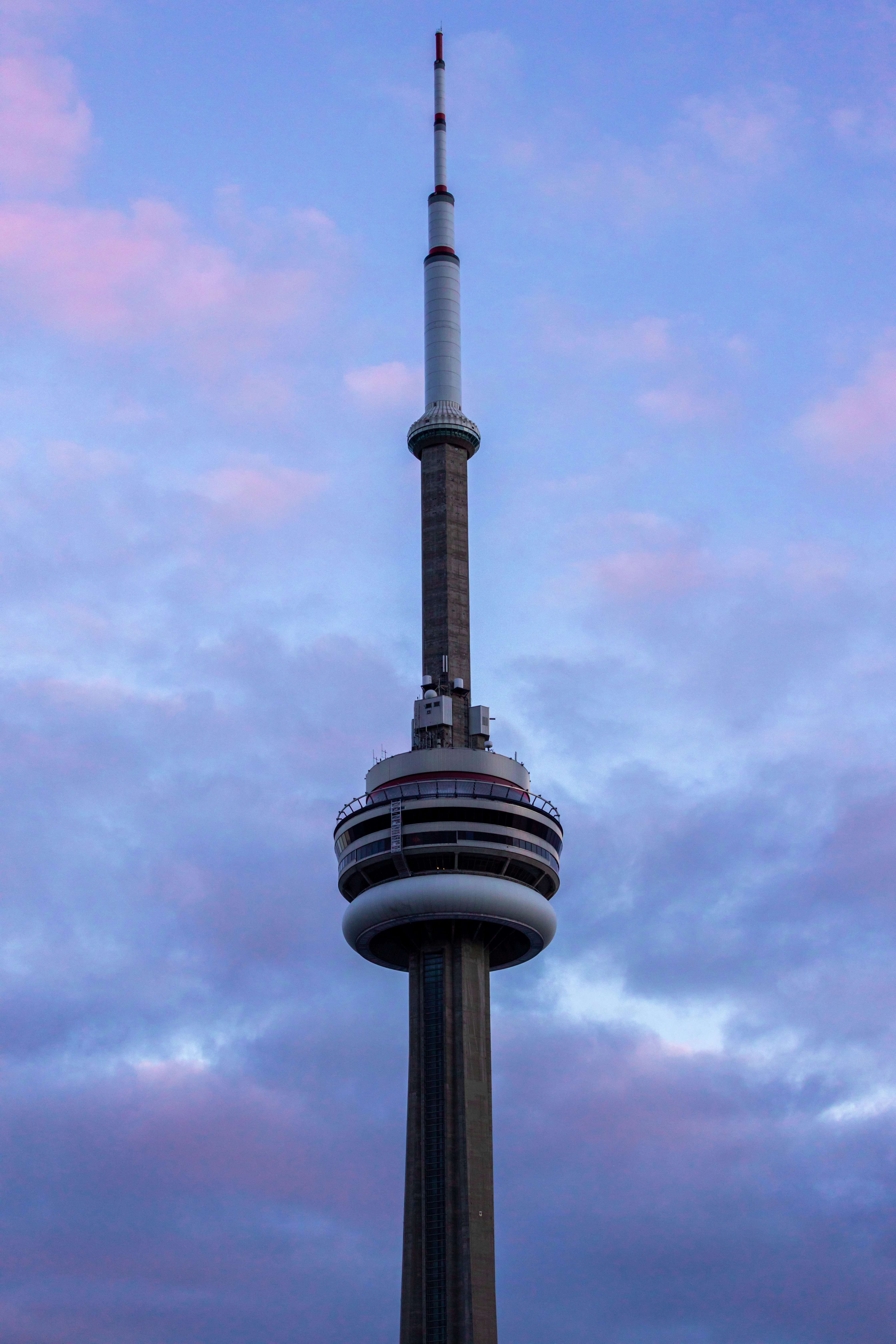 The CN Tower stands tall against a backdrop of soft pastel clouds, showcasing its iconic silhouette. The tower's observation deck is prominently featured.