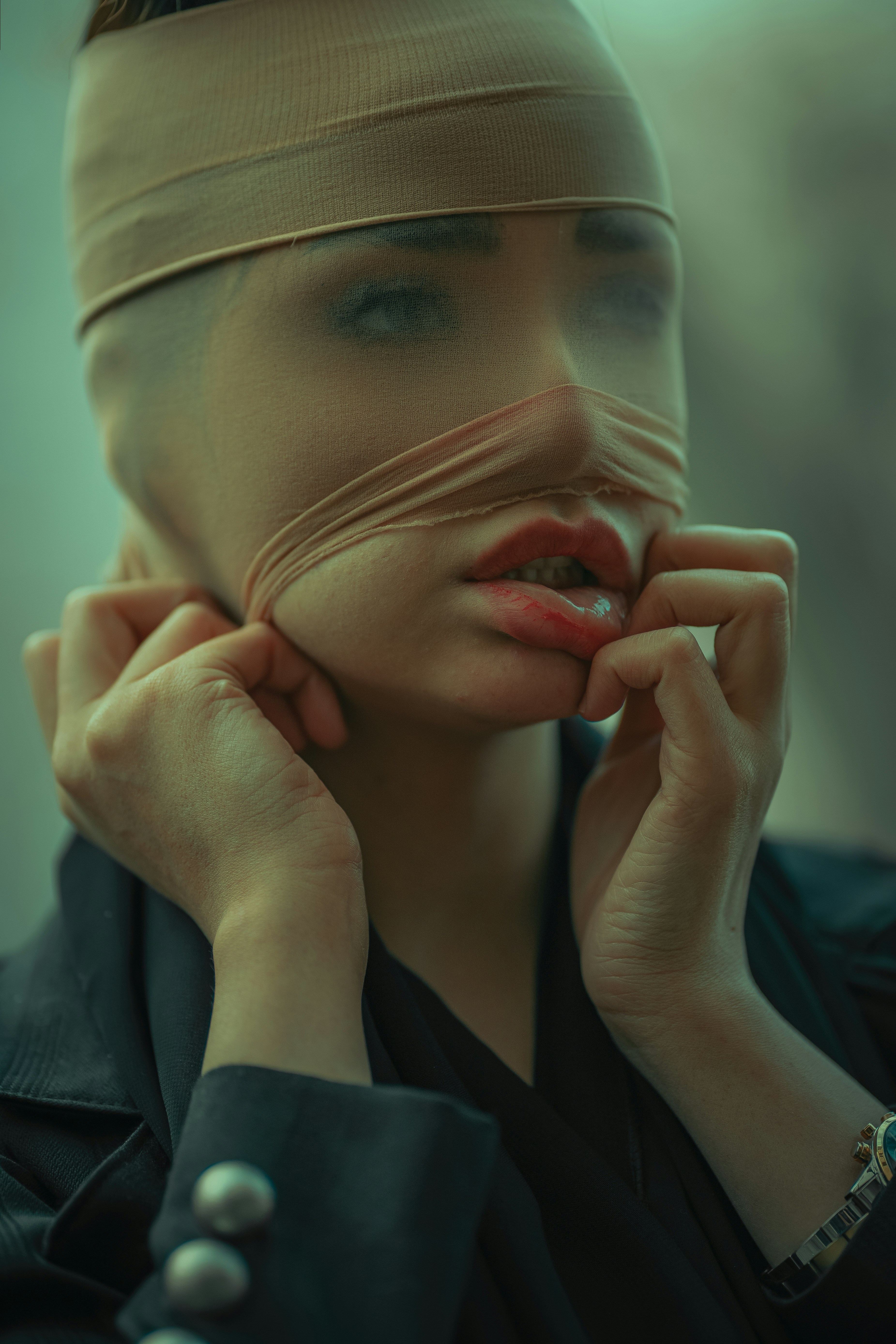 A close-up portrait featuring a model with a sheer fabric covering her face, evoking themes of mystery and vulnerability. The model's hands frame her face, enhancing the emotional depth.