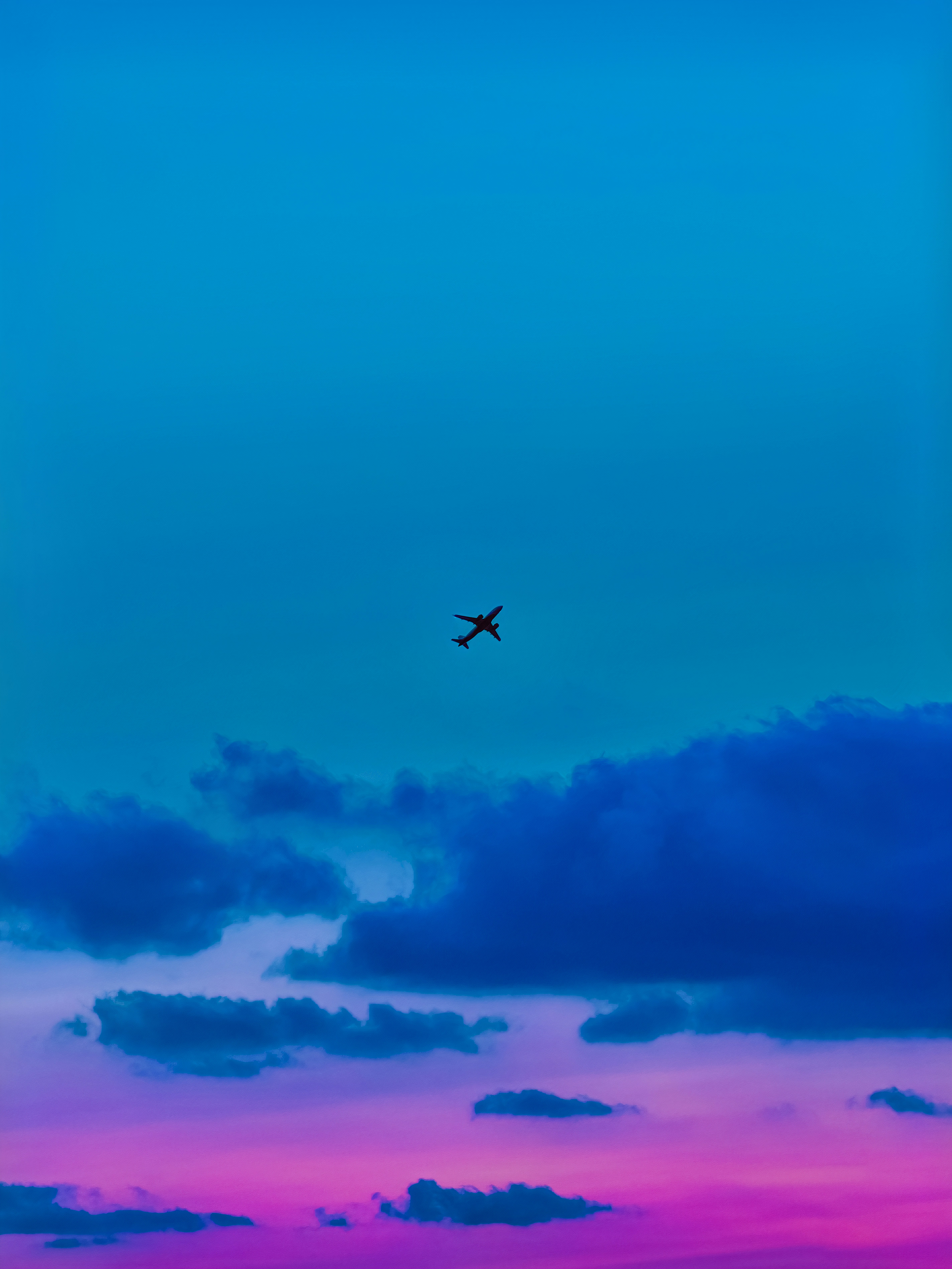 An airplane glides through a vibrant sky painted in shades of blue and pink, silhouetted against the colorful clouds.