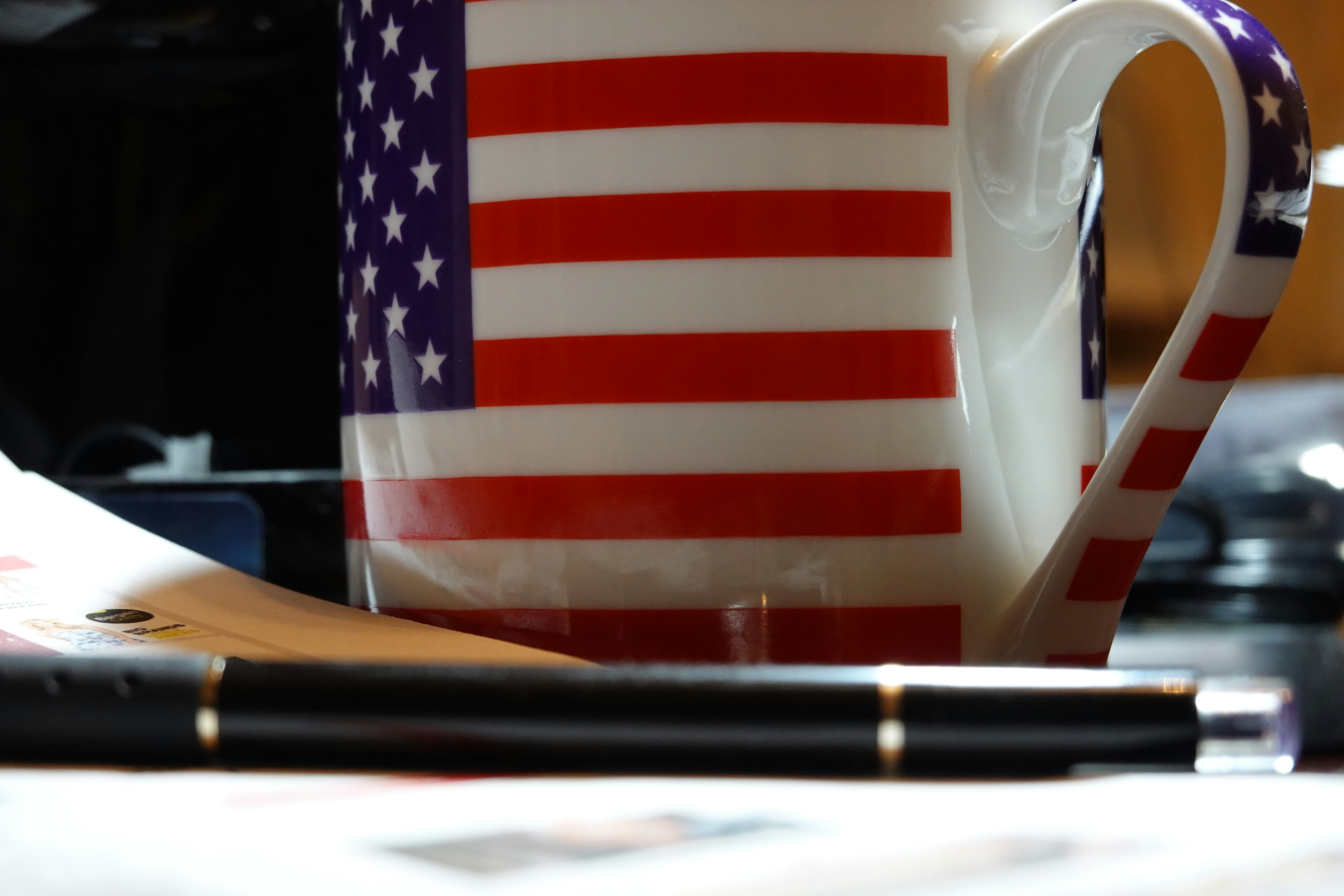 A patriotic mug adorned with the American flag sits on a table, accompanied by a sleek pen and scattered papers. The scene captures a moment of daily inspiration.