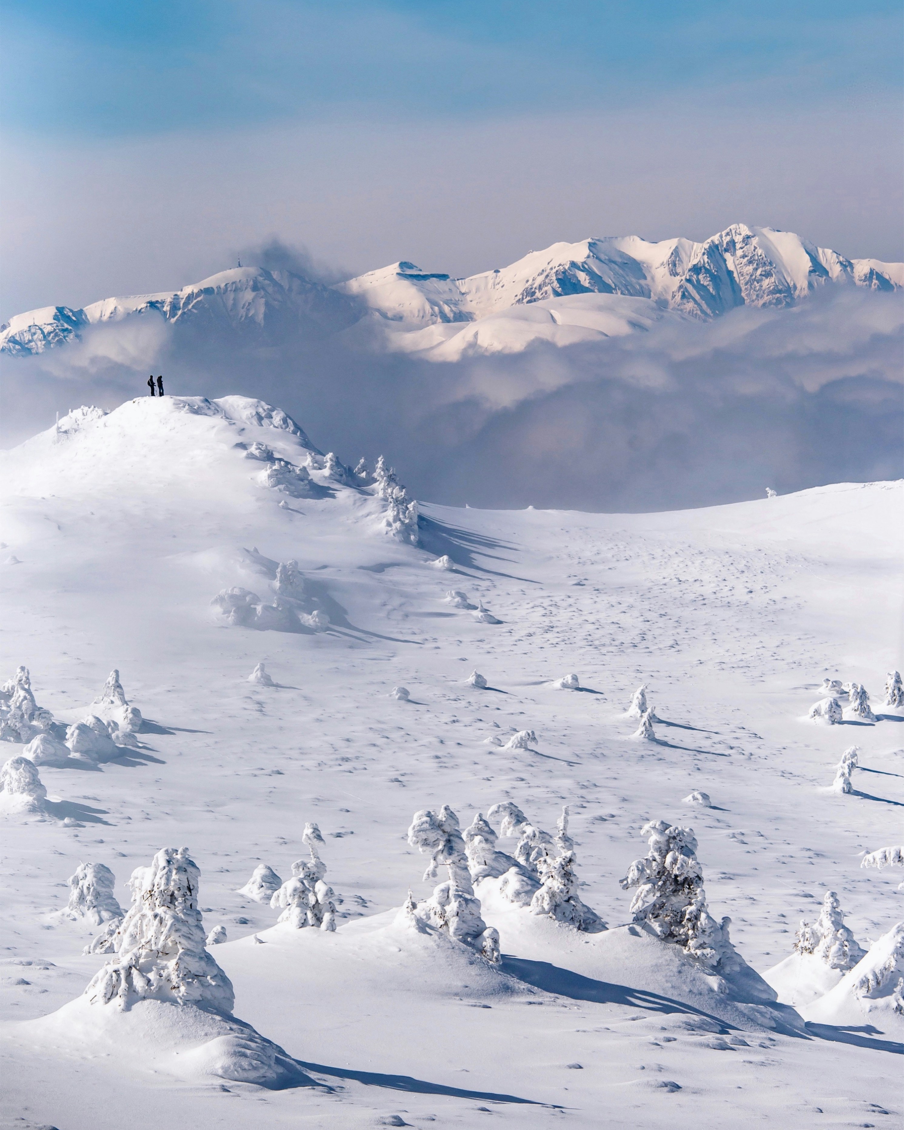 Two Silhouettes Above the Sea of Clouds on a Snow-Capped Spine