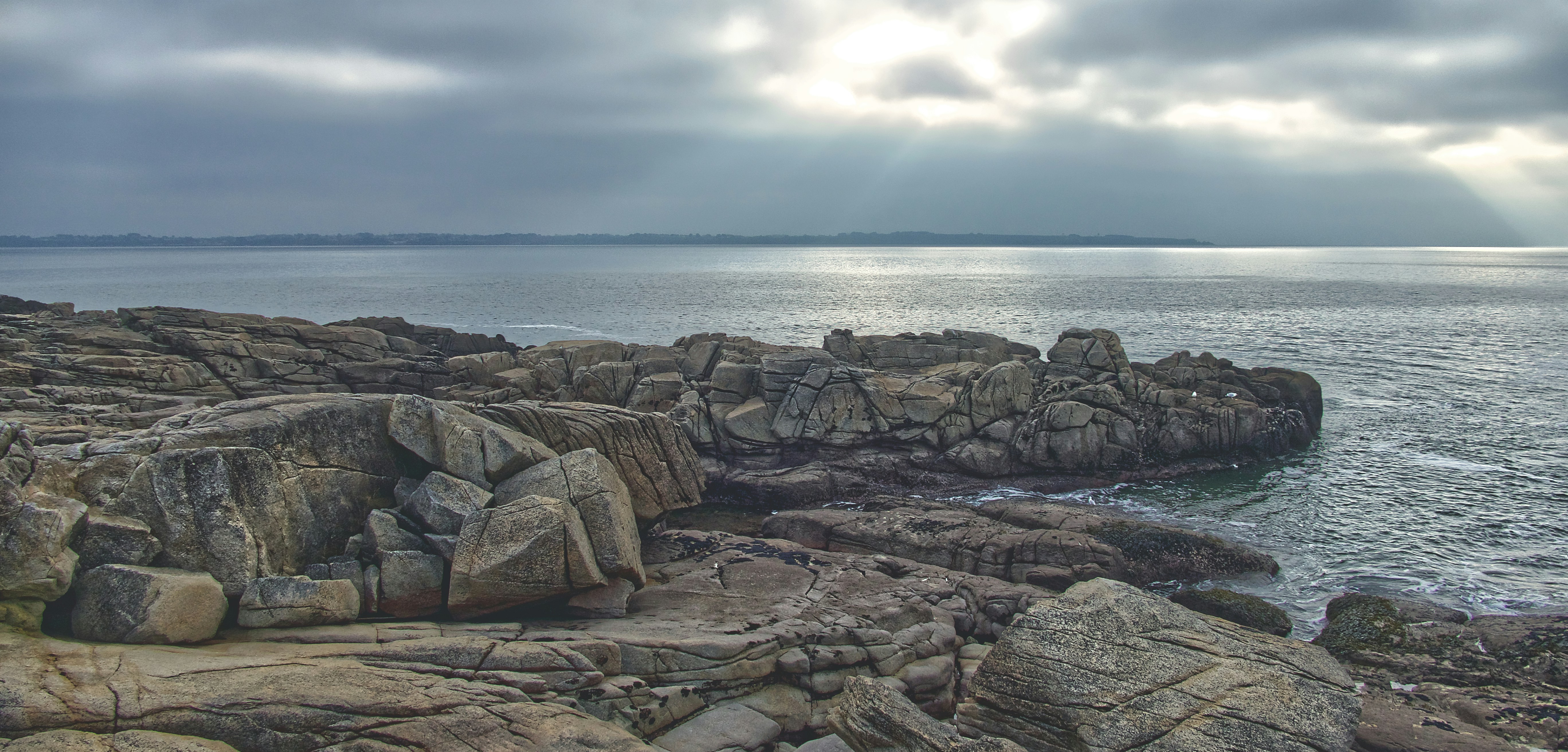 Rugged Rocks Meet a Quiet Horizon as Light Splits the Cloudy Sky