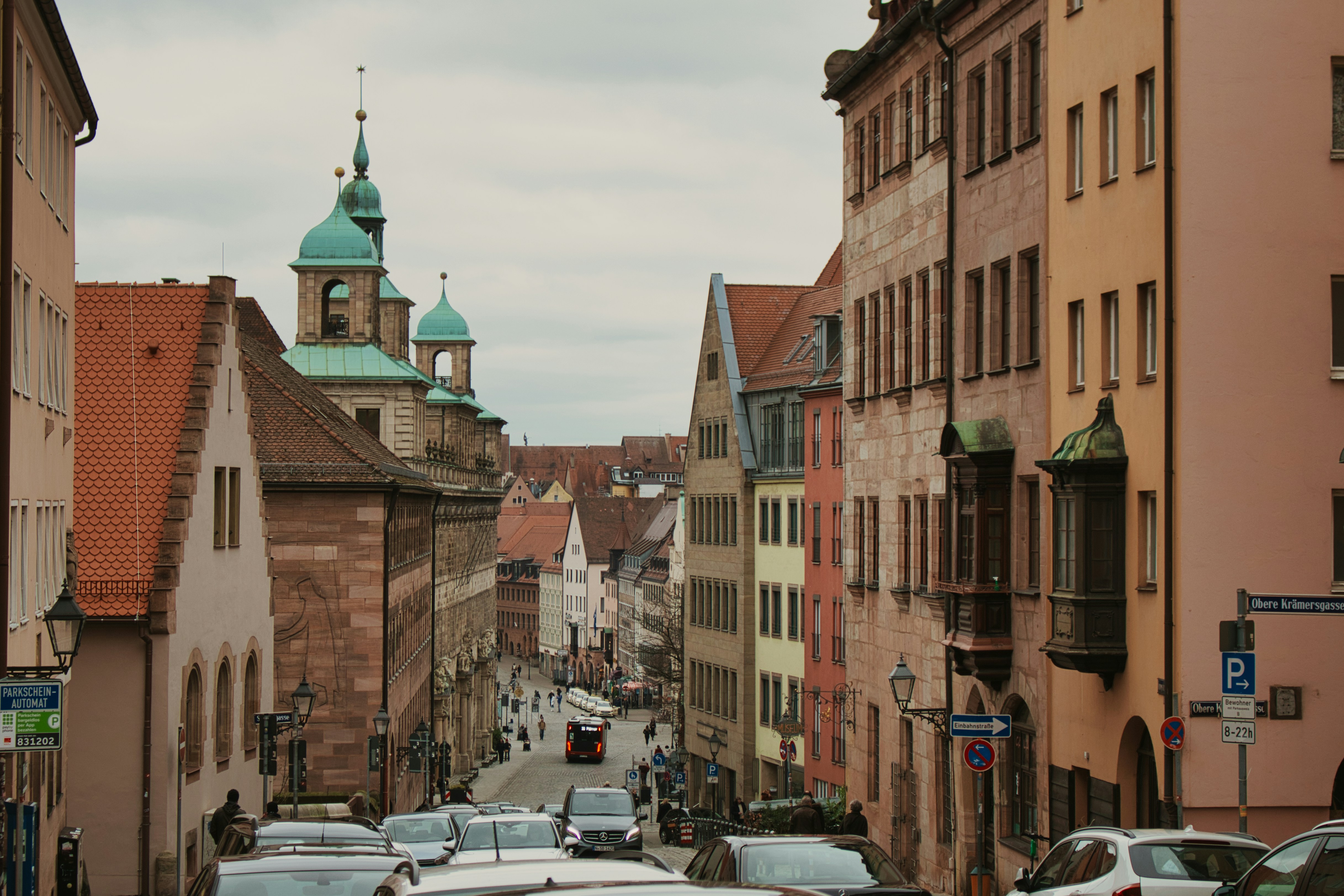 Cobblestone street lined with colorful historic buildings and church towers under a cloudy sky.