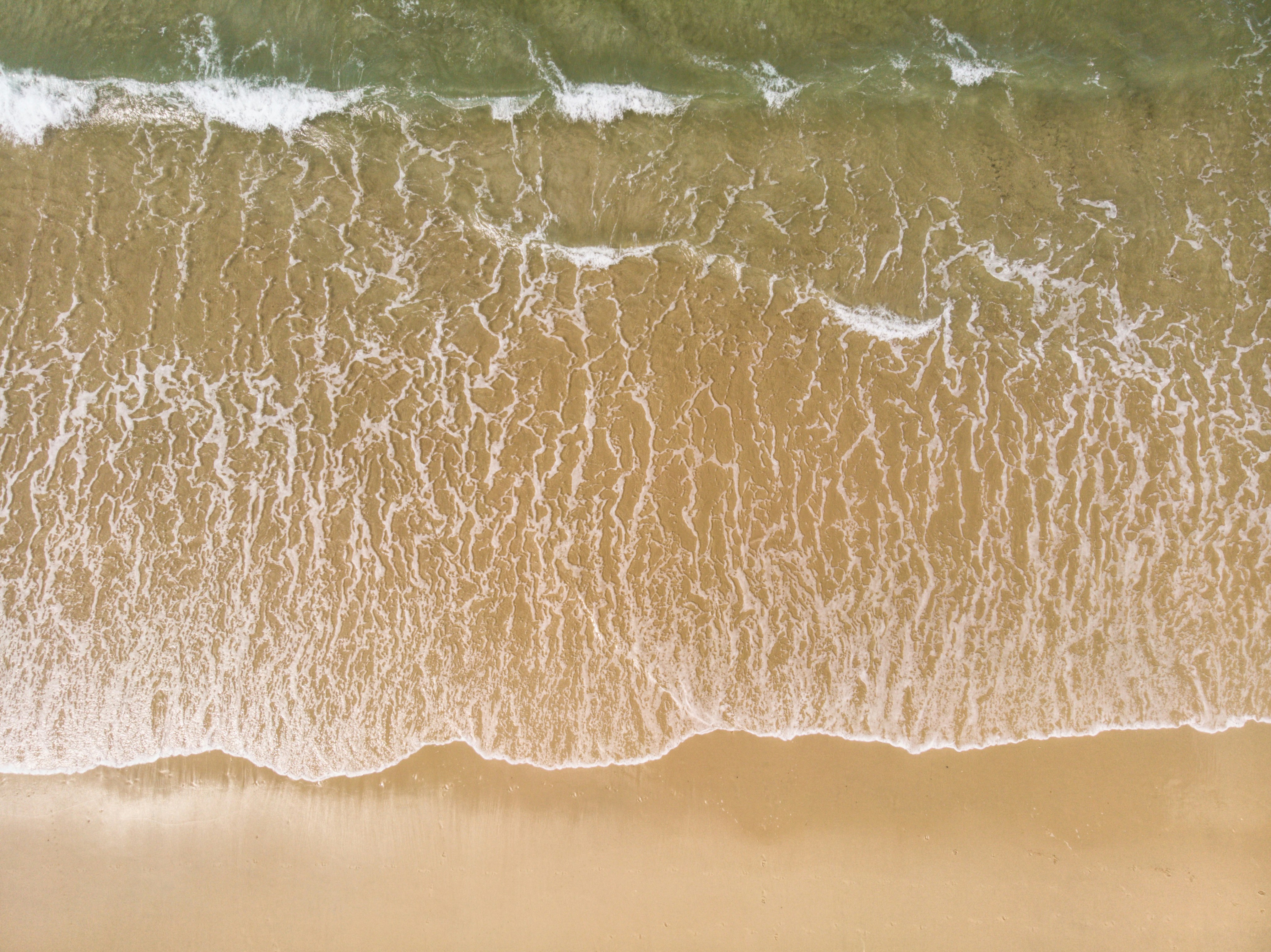 Gentle waves caressing a sandy beach from an aerial perspective, showcasing the intricate patterns of water and sand. 